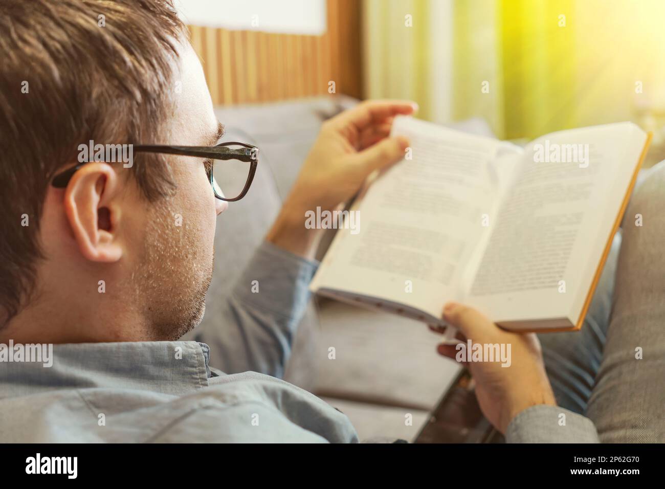 leisure, literature and people concept - man sitting on sofa and ...