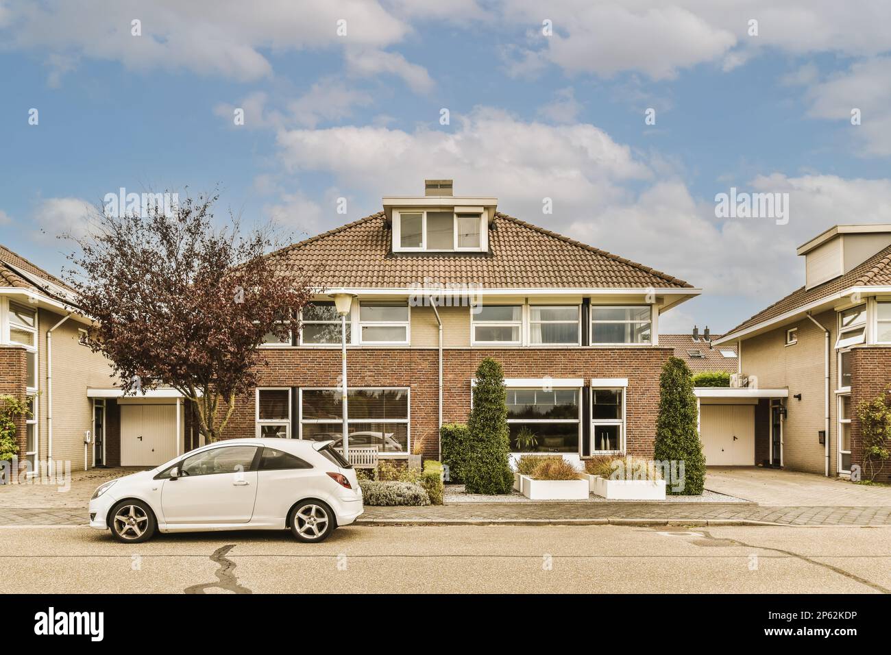 a house with a car parked in the driveway next to it and some bushes on ...