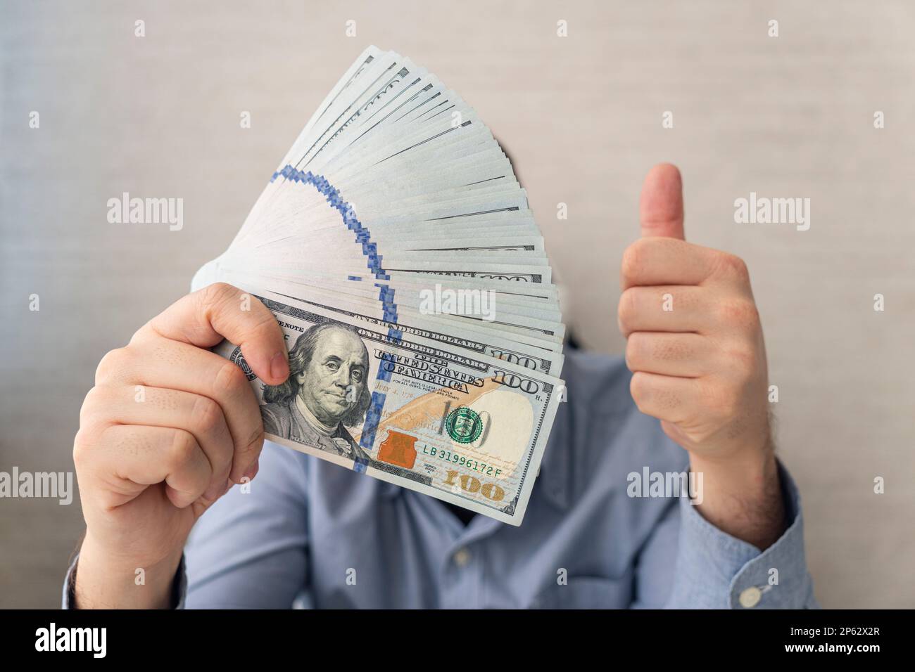 Happy young man in a blue t-shirt holding money and showing thumbs up ...