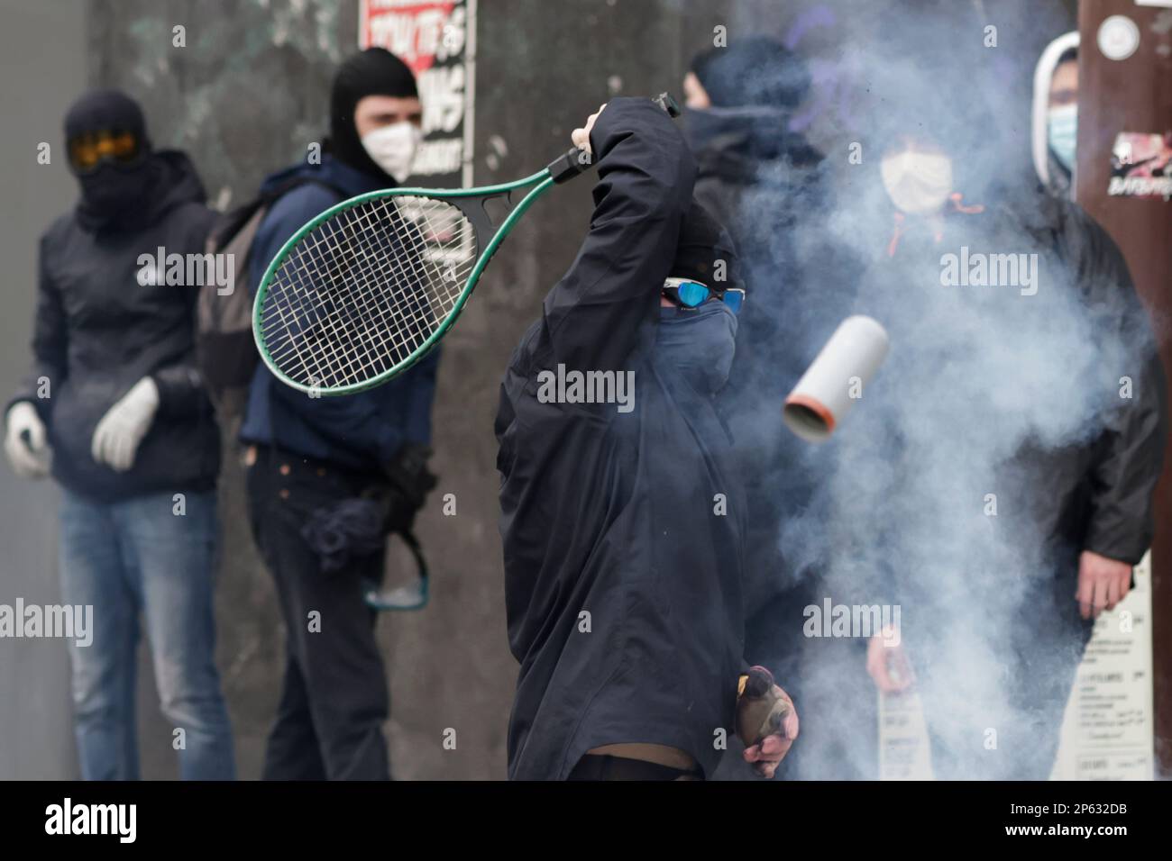A youth uses a tennis racket to throw a gas canister to police forces ...