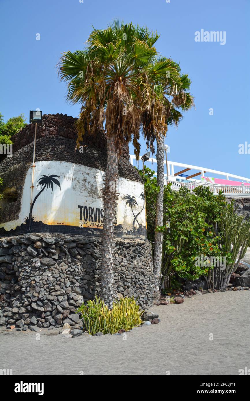Torviscas Playa lettering on a stone wall on the beach, with palm trees ...