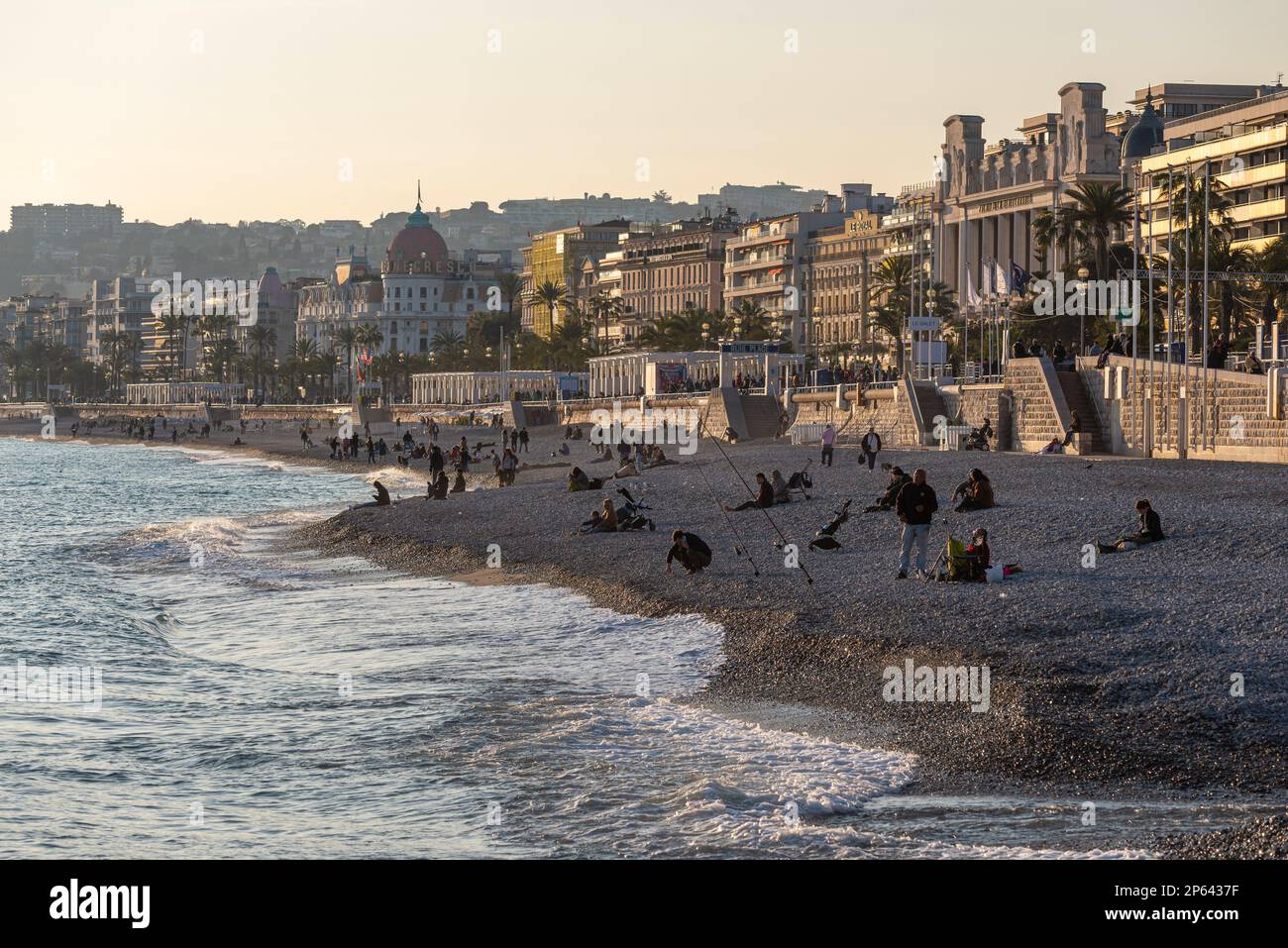 Tourists and fishers enjoying the sunset over the pebble beach of Nice ...