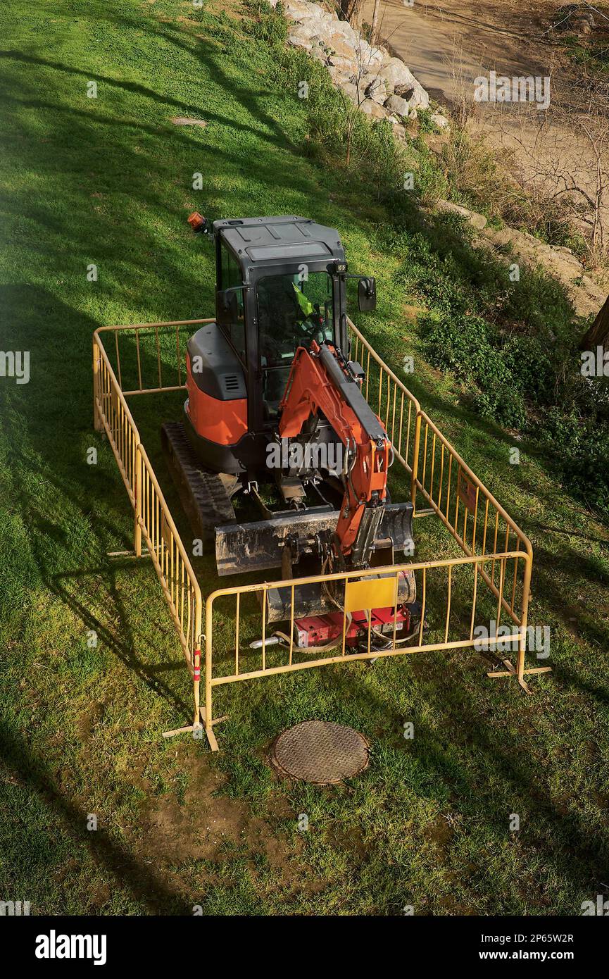 Mini excavator surrounded by fence above ground in a field or forest ...