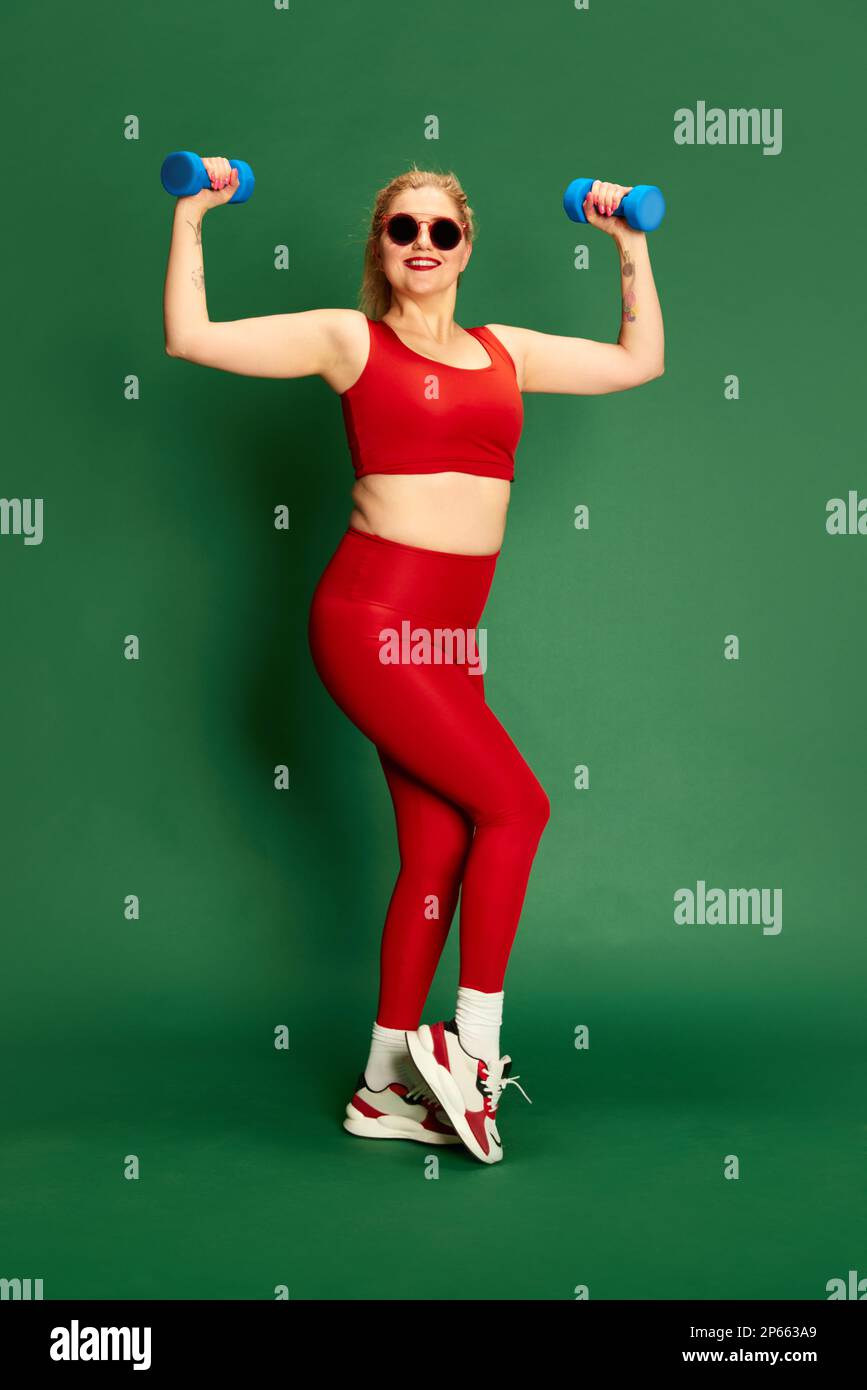 Full-length portrait of woman in red sportive clothes posing, training ...
