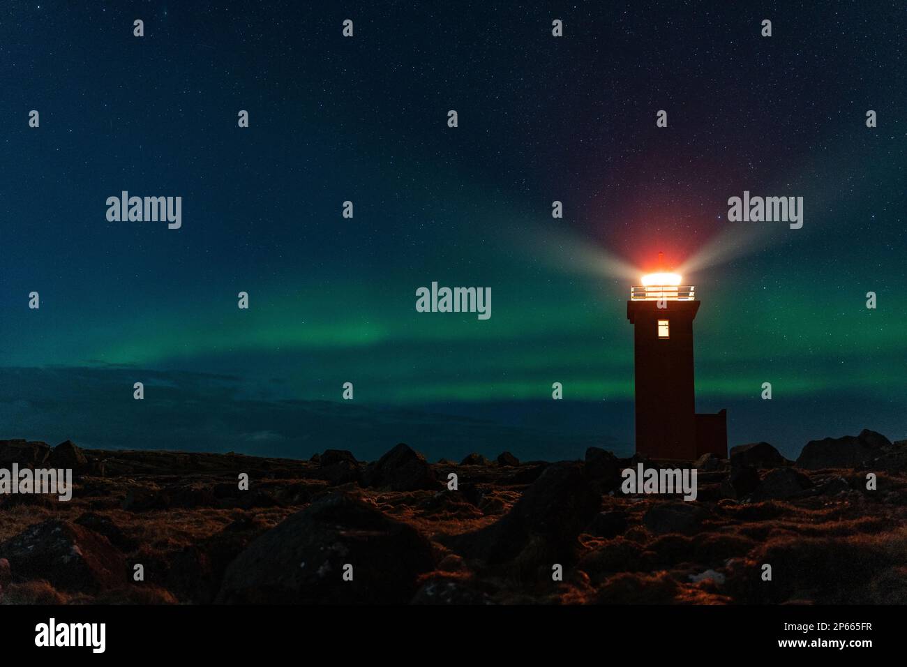 A majestic lighthouse stands on a rocky shoreline, illuminated by an ...