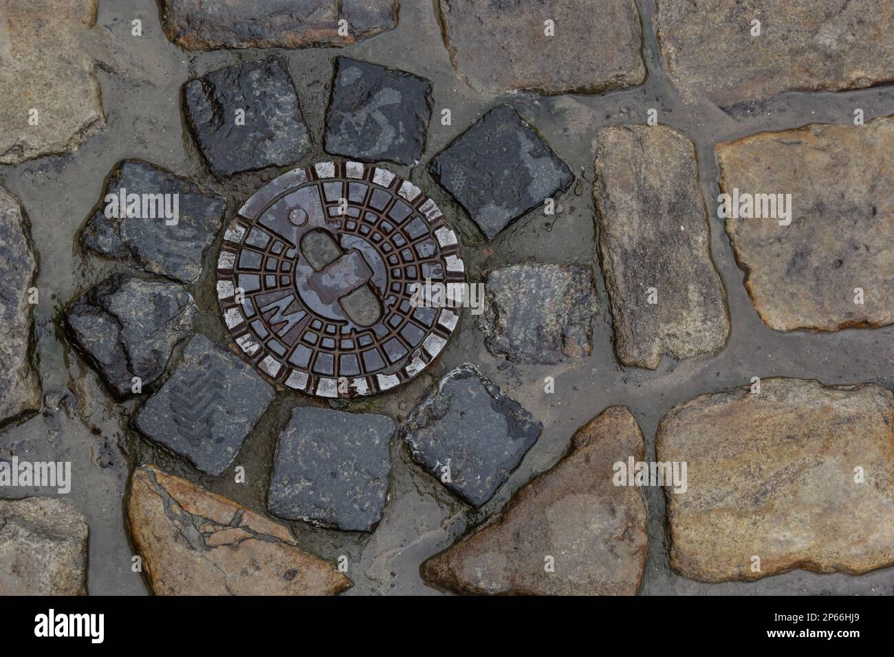 Old metal sewer hatch in the middle of the road, laid out of a smooth ...