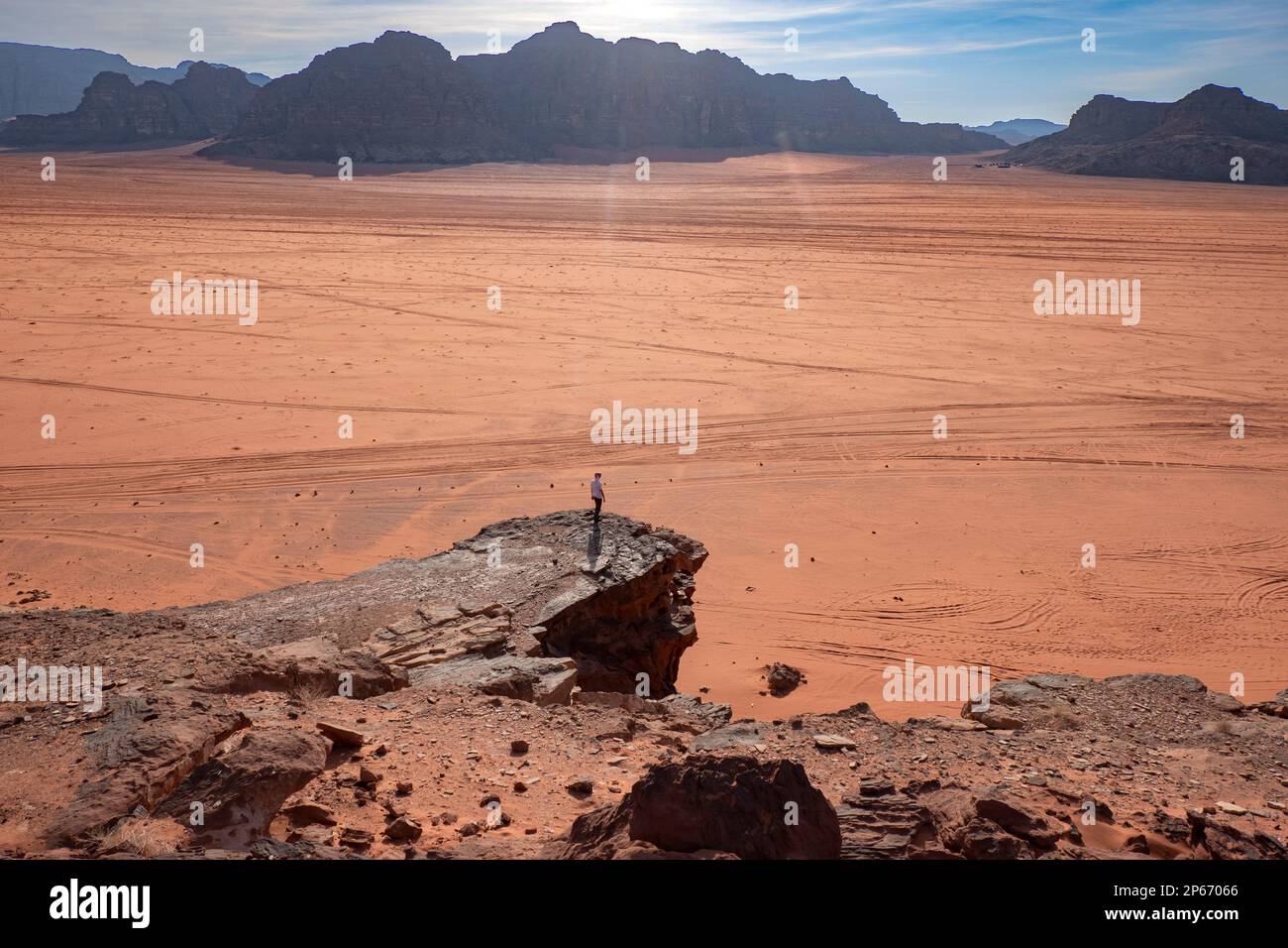 A person standing on a rock above the wide plain of Wadi Rum desert ...