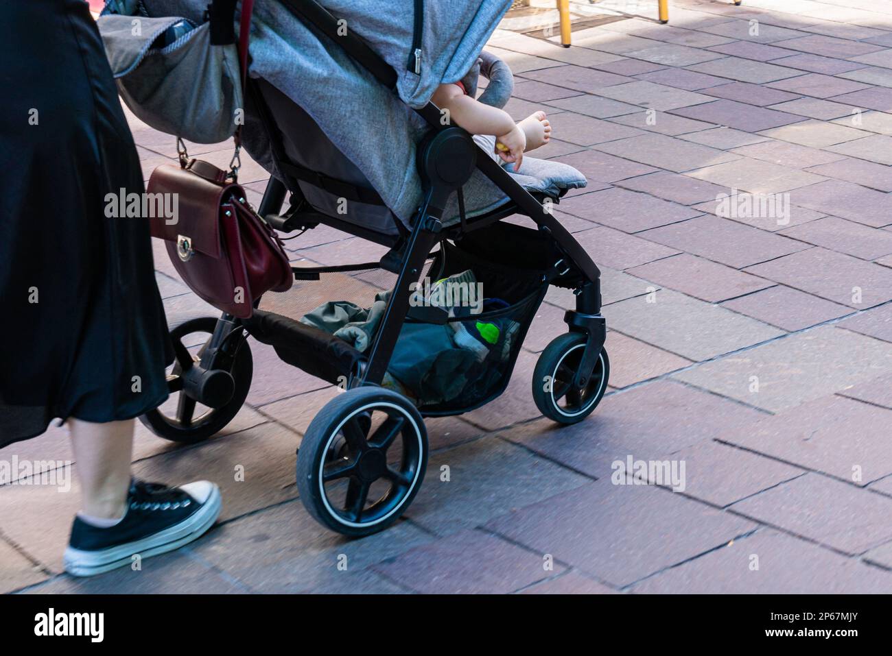 Woman with baby stroller walks in the city. Only the child's arm and ...