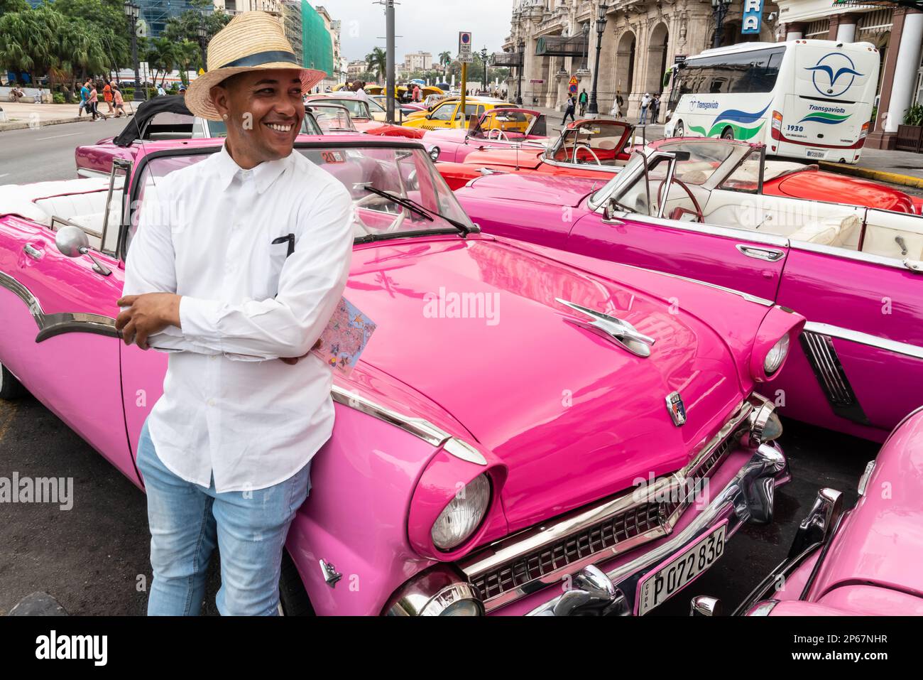 Taxi driver amidst many parked classic cars, Havana, Cuba, West Indies ...