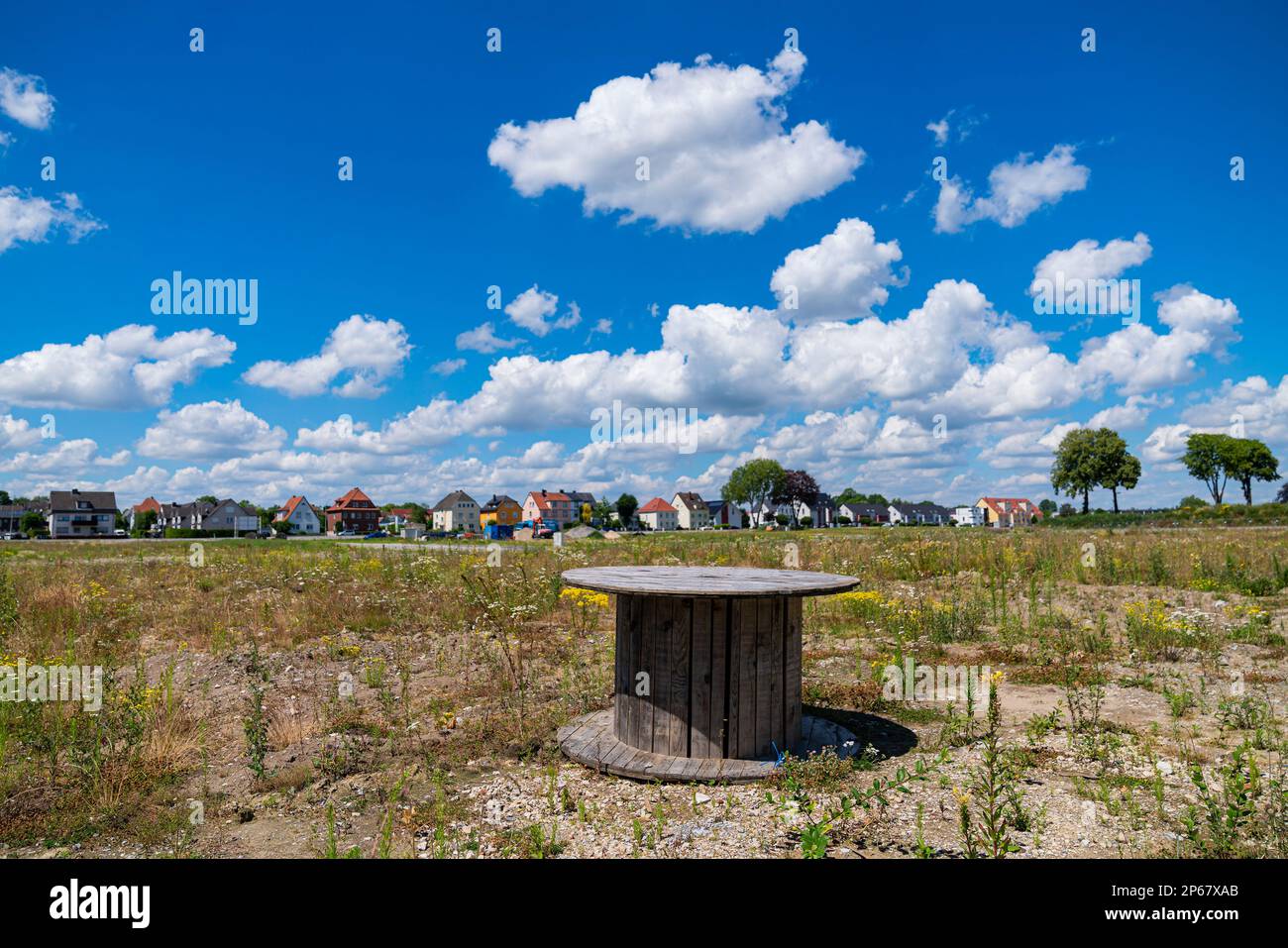 An empty cable spool lying on a wasteland. Houses in the background ...