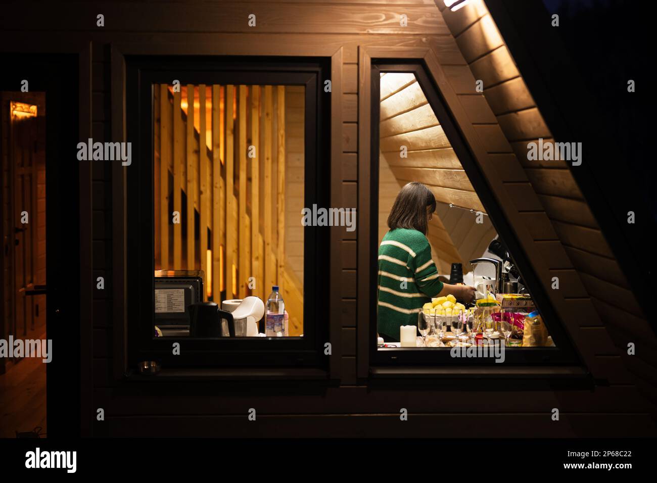 Woman prepares dinner in the kitchen, a view through the window of a ...