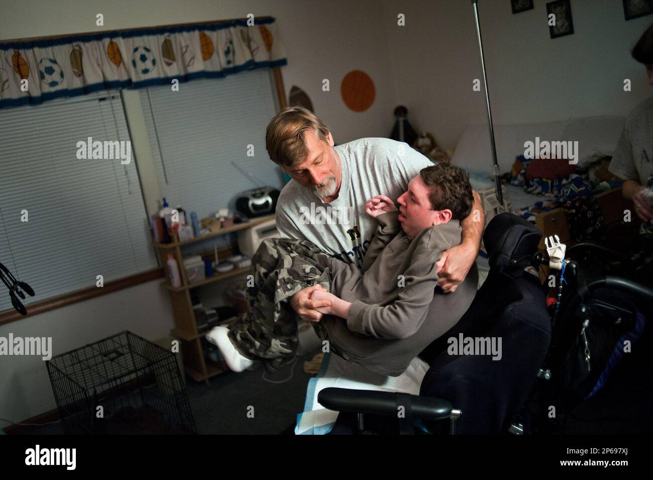 Ron Riker carries his 16-year-old son, Bryan into his chair after ...