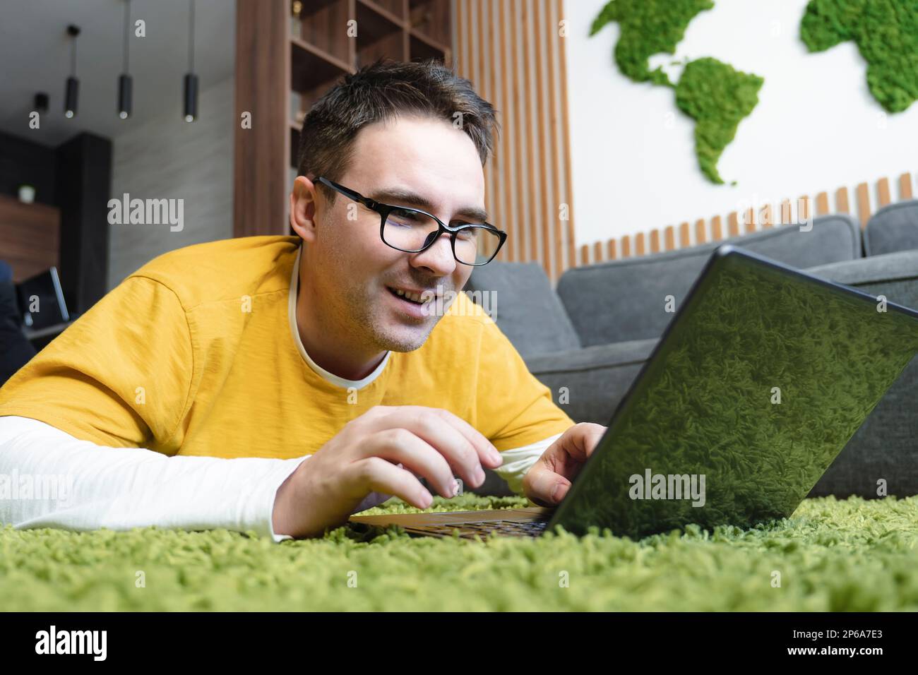Handsome young man laying on floor at home, browsing internet smiling ...