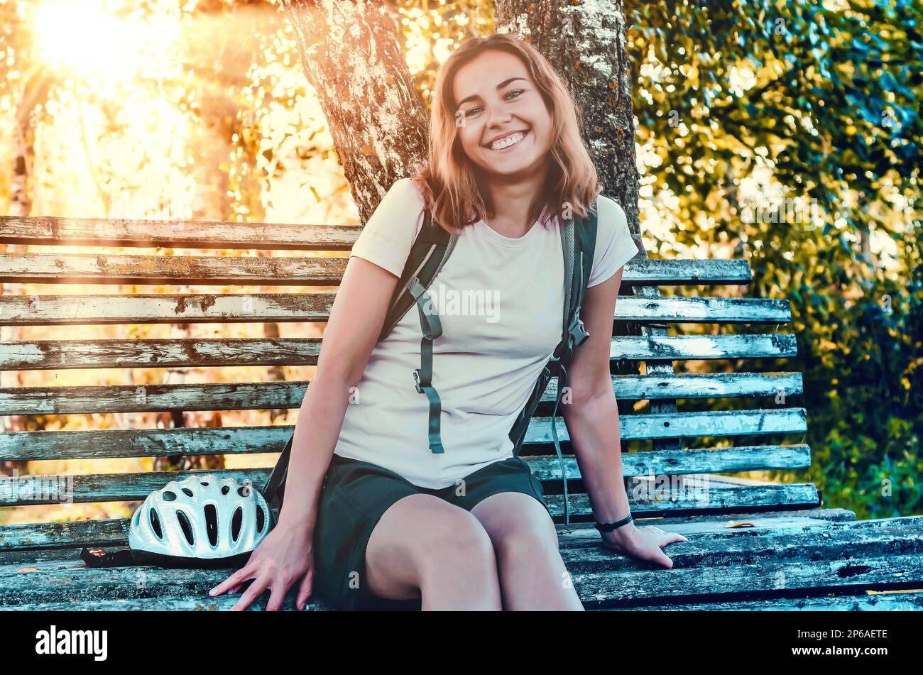 woman in a sports uniform is resting after a bike ride on an old bench ...