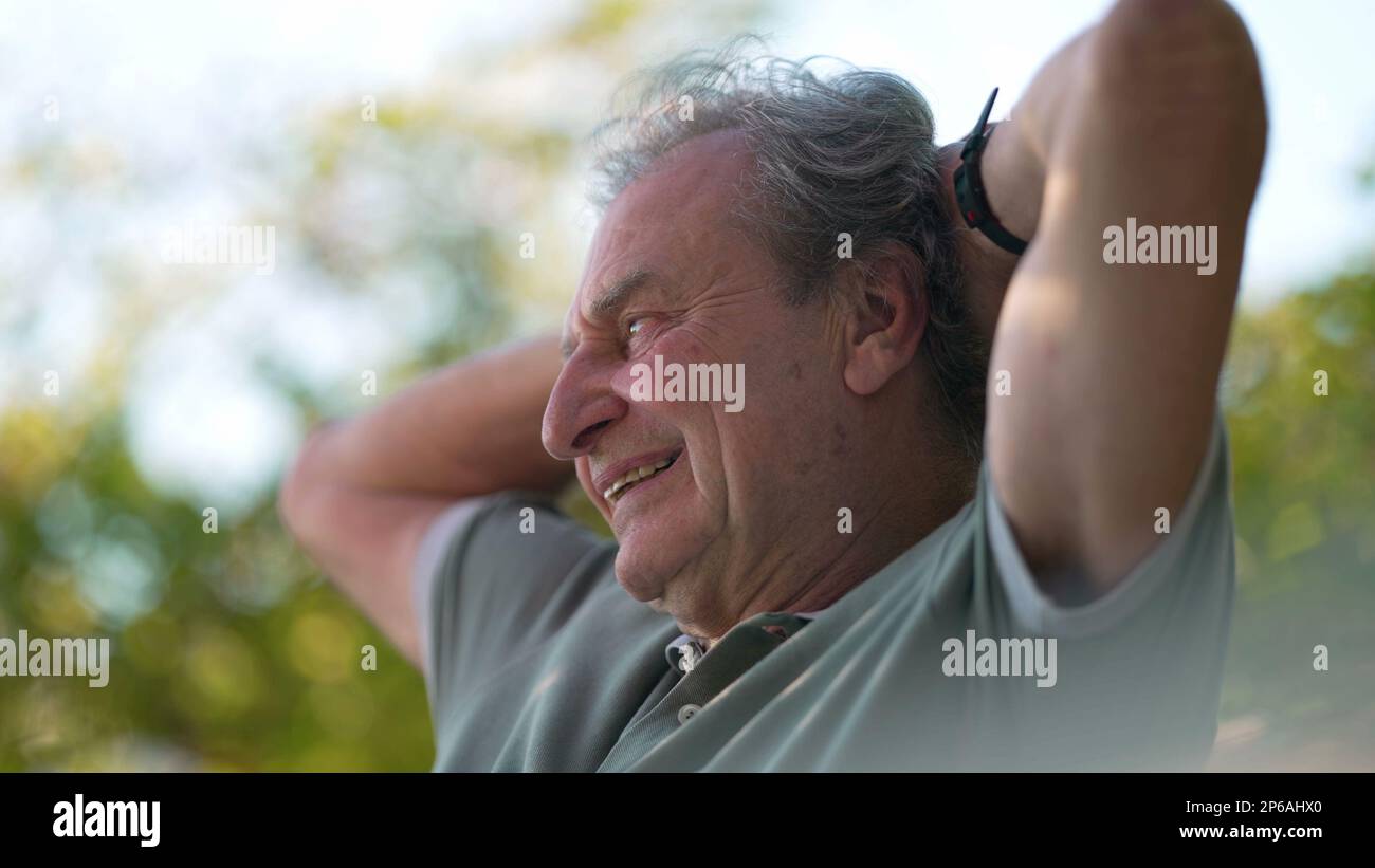 One relaxed happy retired senior man at outdoors park with hands behind ...