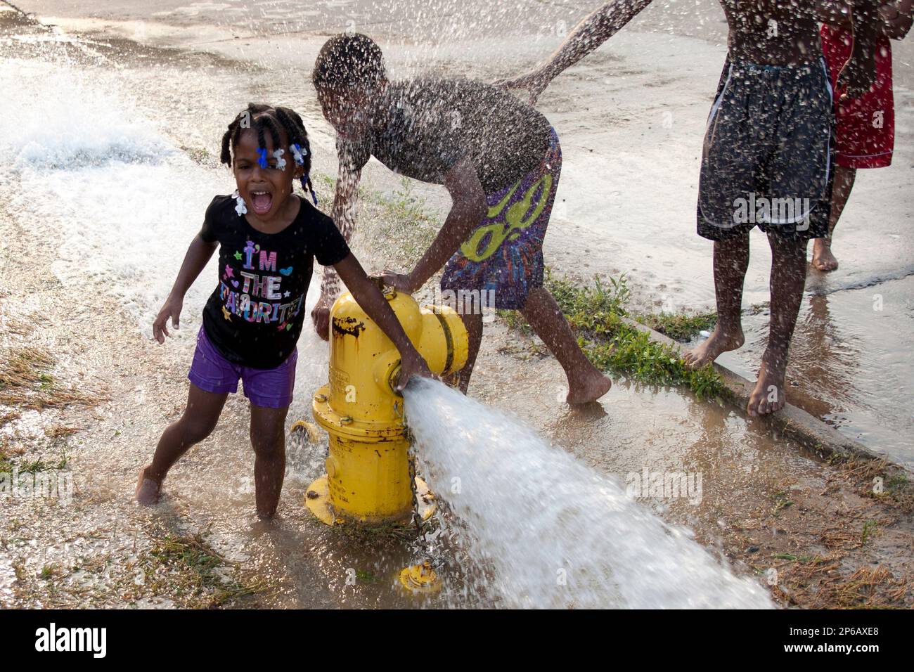 Children play in a opened fire hydrant in the late afternoon in Flint ...