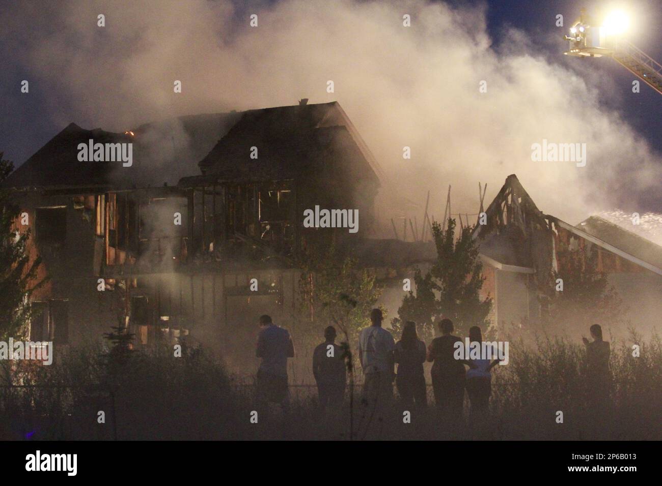 People watch as firefighters work to put down a fully involved house ...