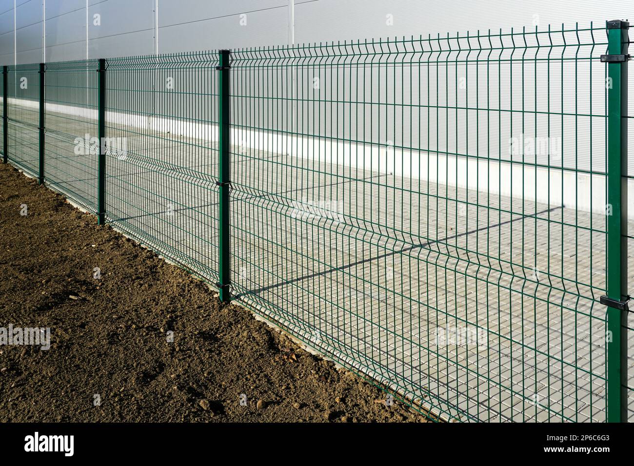 A new green metal grid fence around a new industrial site, grass soil ...