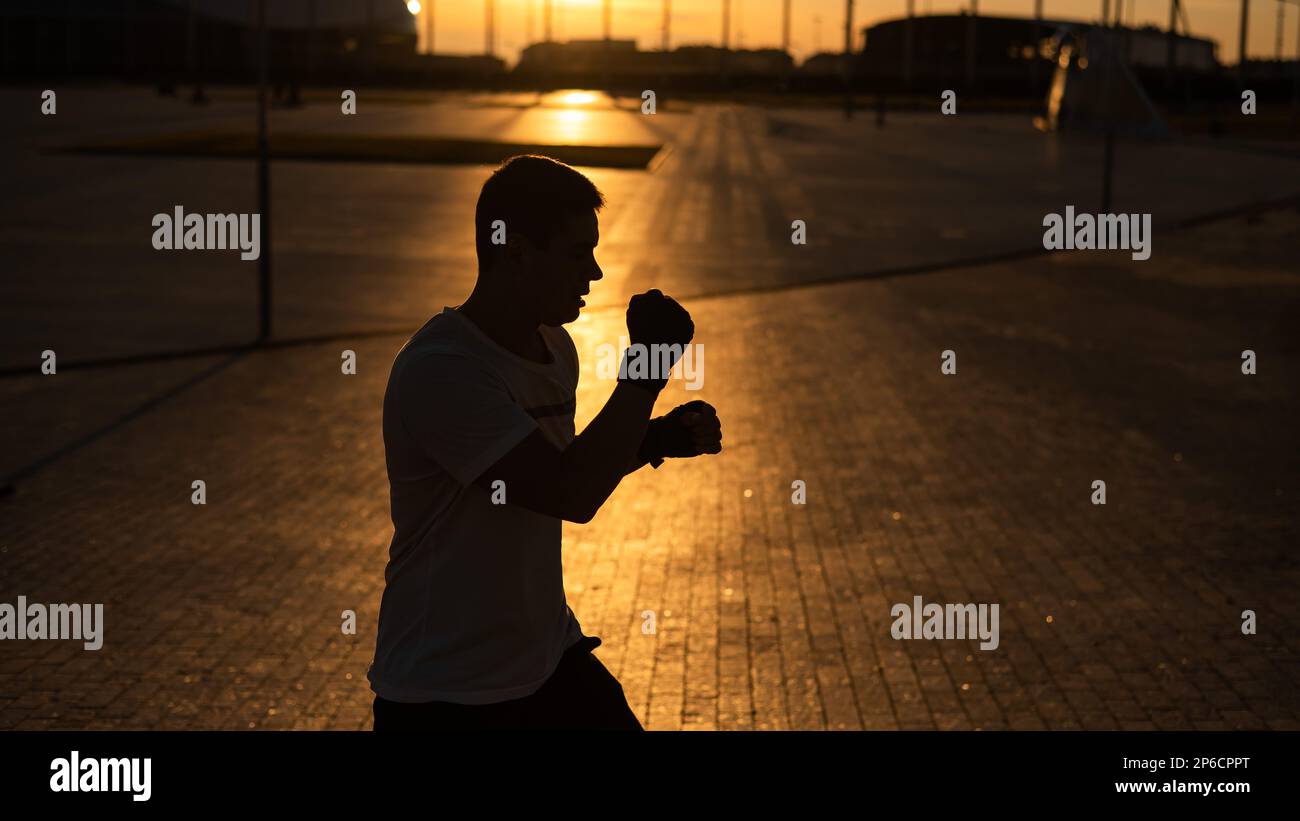 A man trains in boxing at the stadium at sunset. Athlete silhouette ...