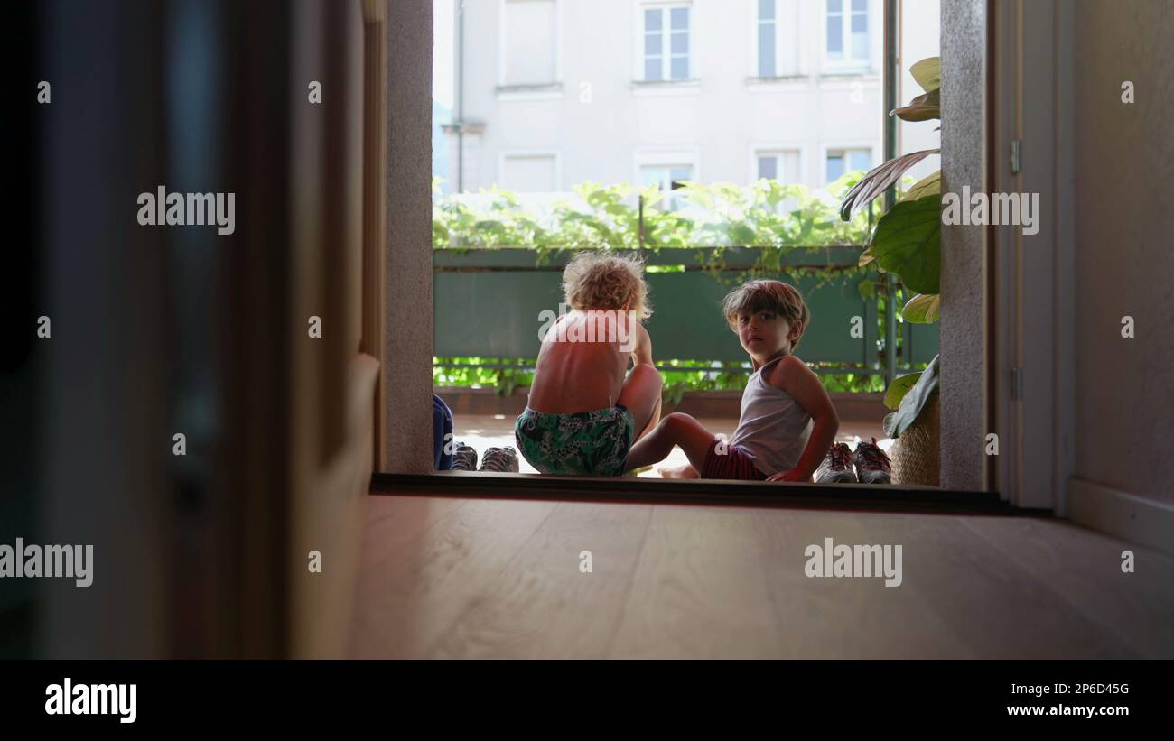 Children sitting by door step putting shoes on outside. Older brother ...