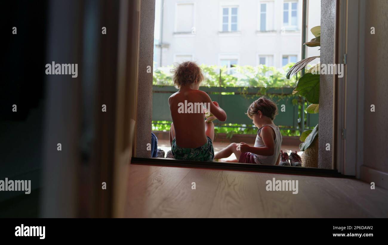 Children sitting by door step putting shoes on outside. Older brother ...