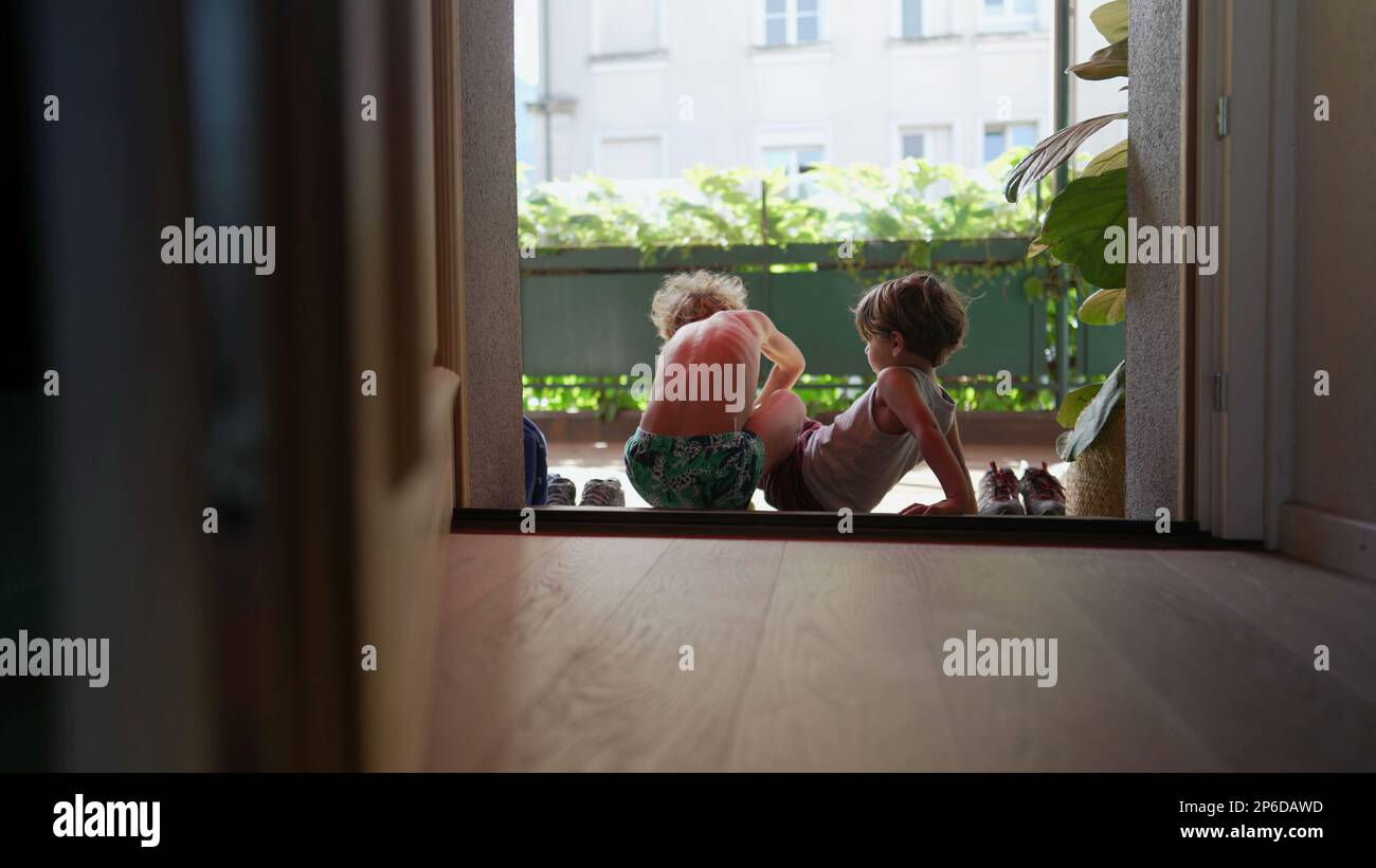Children sitting by door step putting shoes on outside. Older brother ...