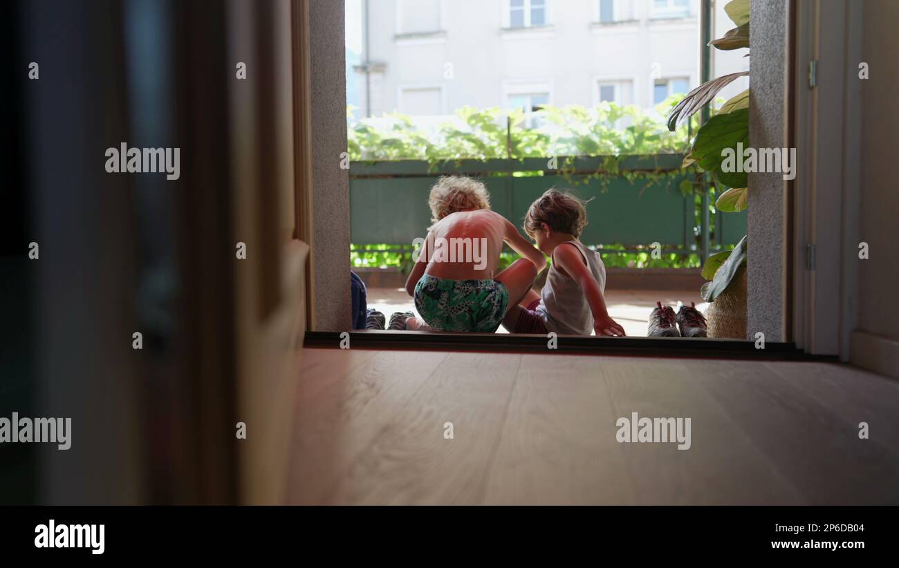 Children sitting by door step putting shoes on outside. Older brother ...