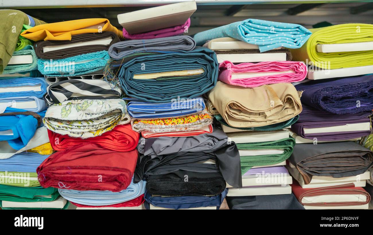 Coils of fabric are on the shelves in the store. Piles of different ...