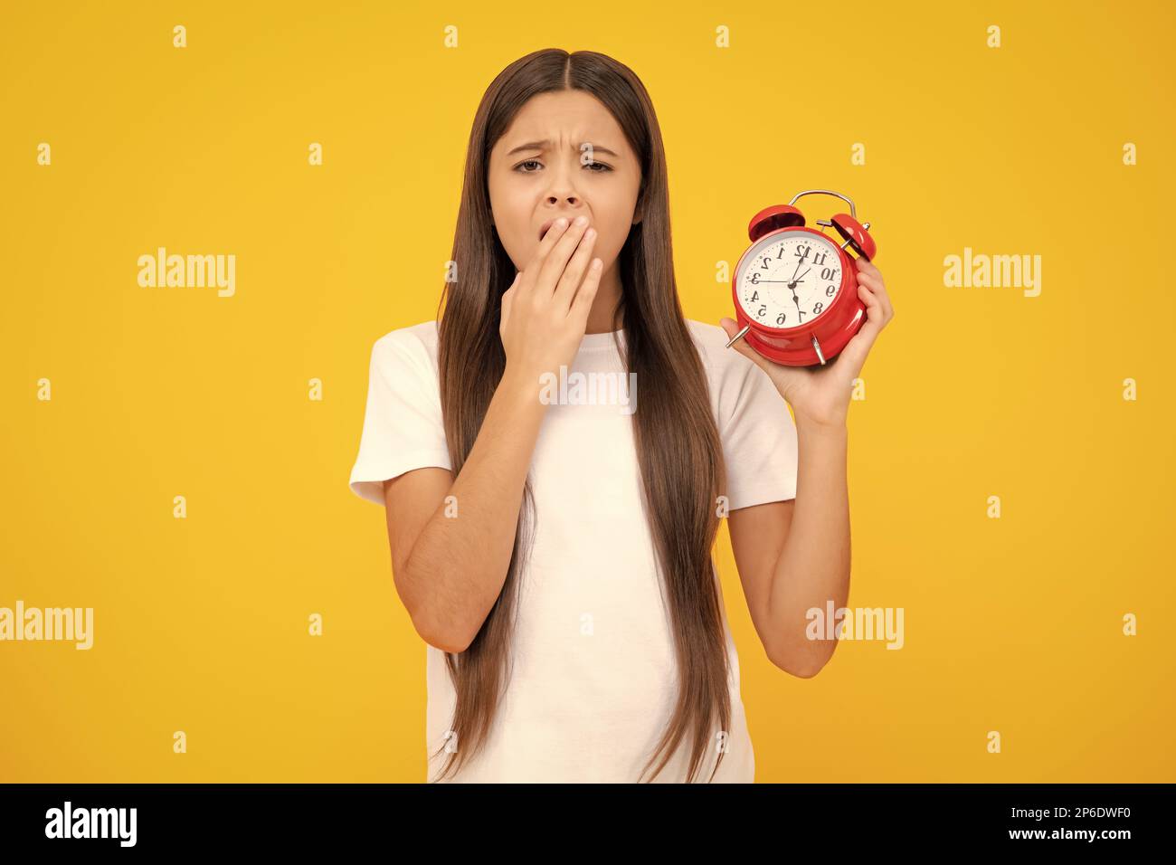 Tired and bored teenager girl. Child holding clock over yellow ...