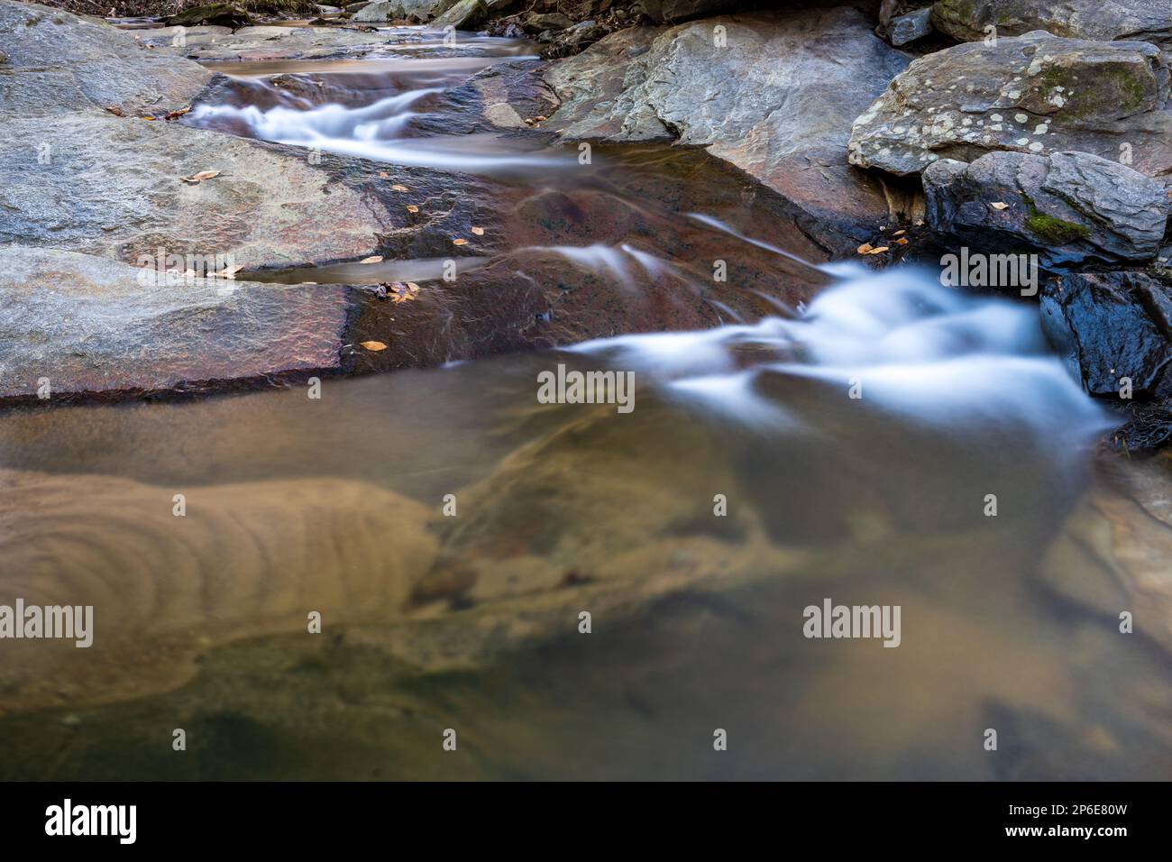 A crystal-clear stream of water cascades over a rocky ledge Stock Photo ...