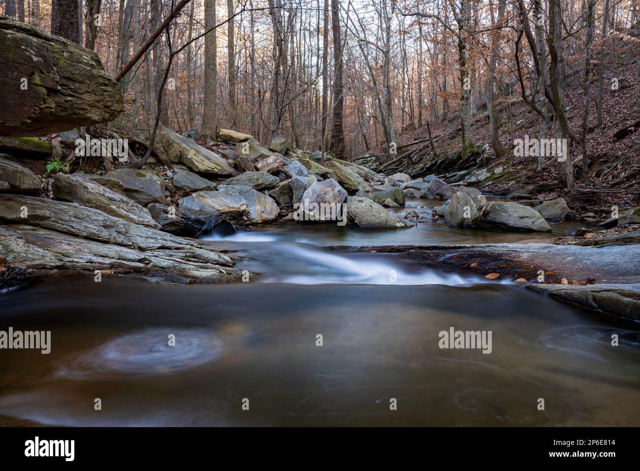A tranquil stream meandering through a fall forest surrounded by jagged ...