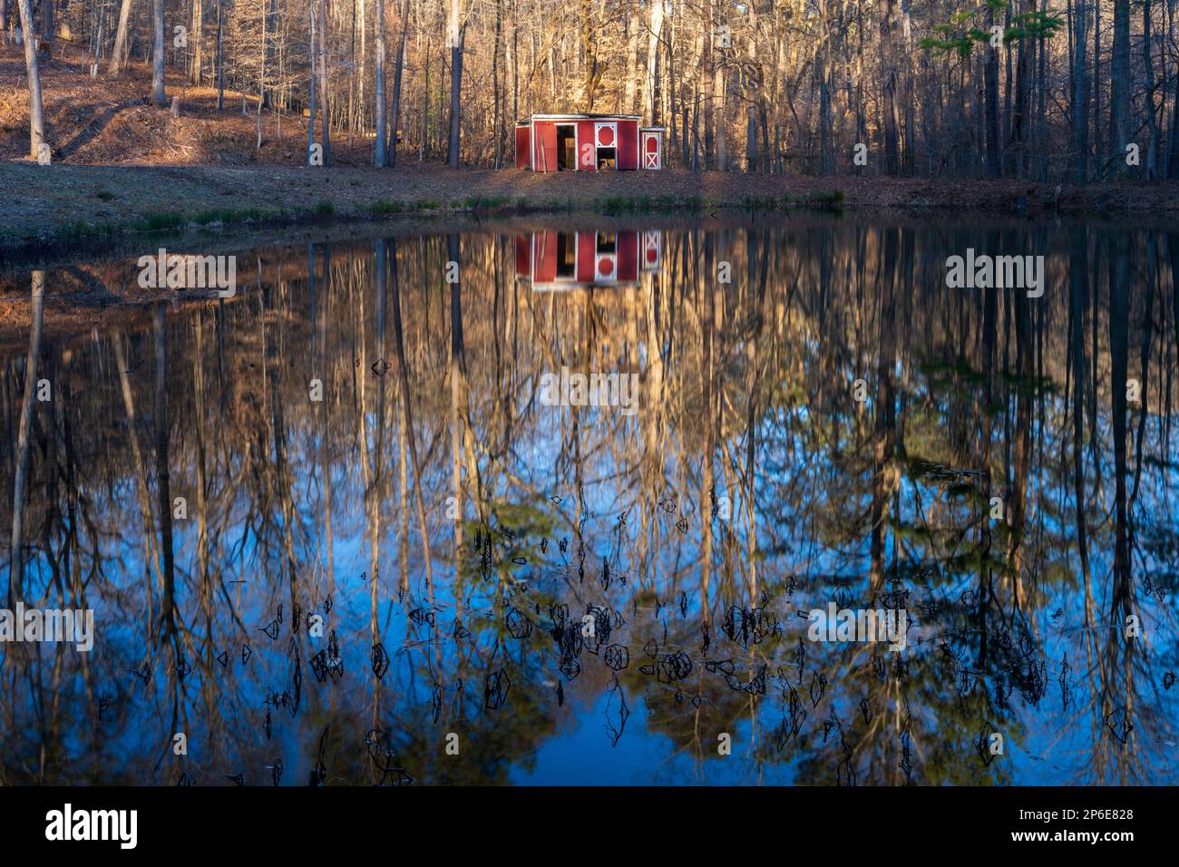 A rustic red boathouse on the edge of a tranquil pond with its ...