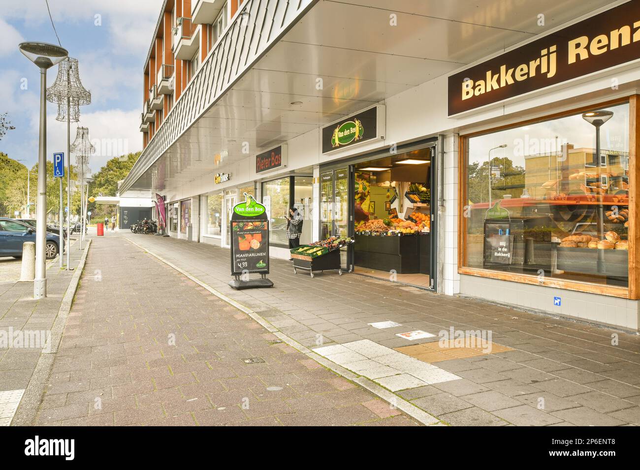 an empty street with cars parked on the side and people walking down ...