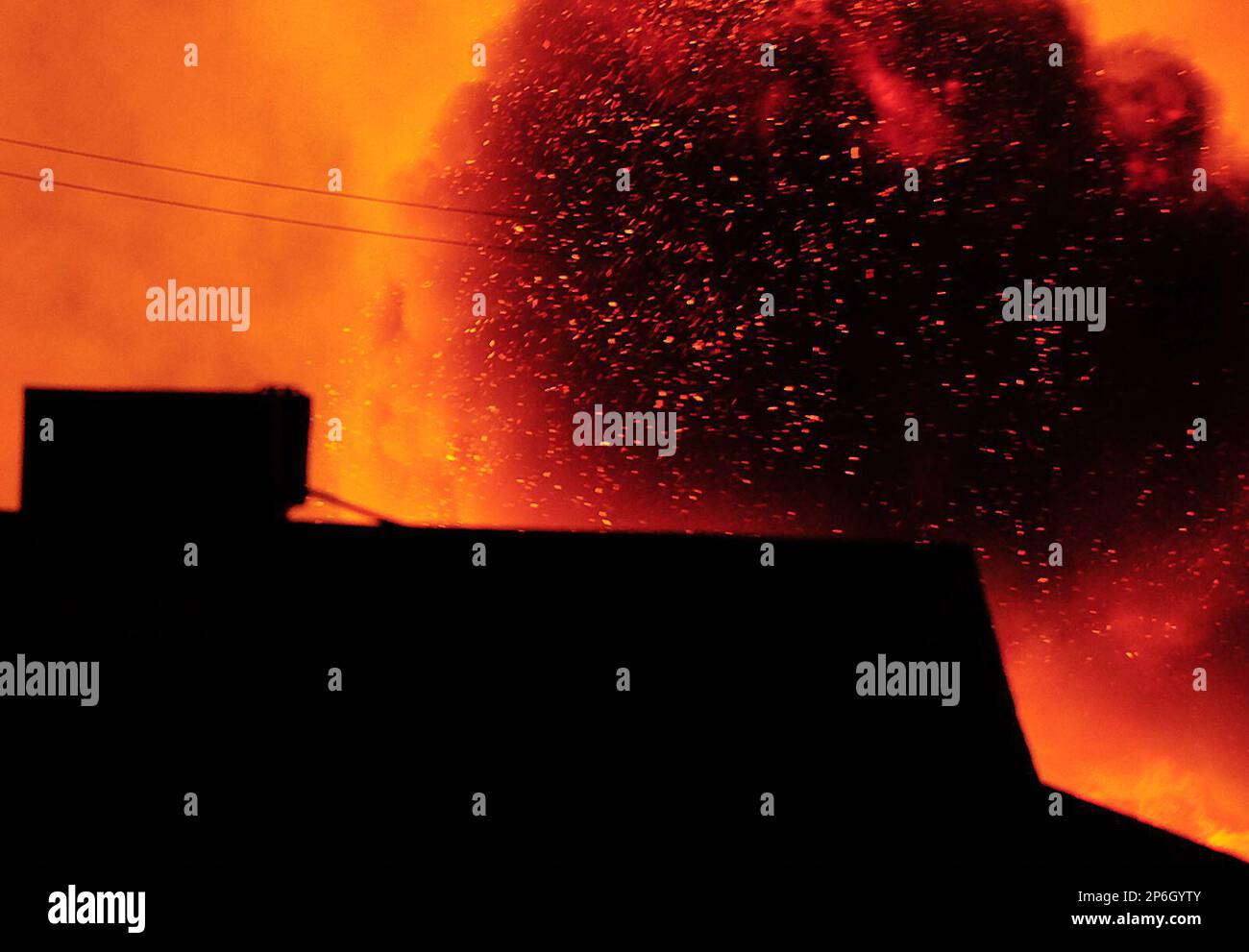 A large ball of smoke rises as hot embers burst from it behind a home ...