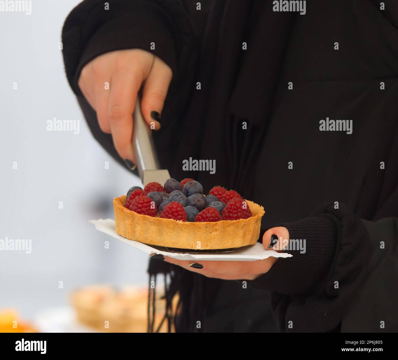 Closeup of a vendor at a pastry stand scooping a tart onto a paper tray ...