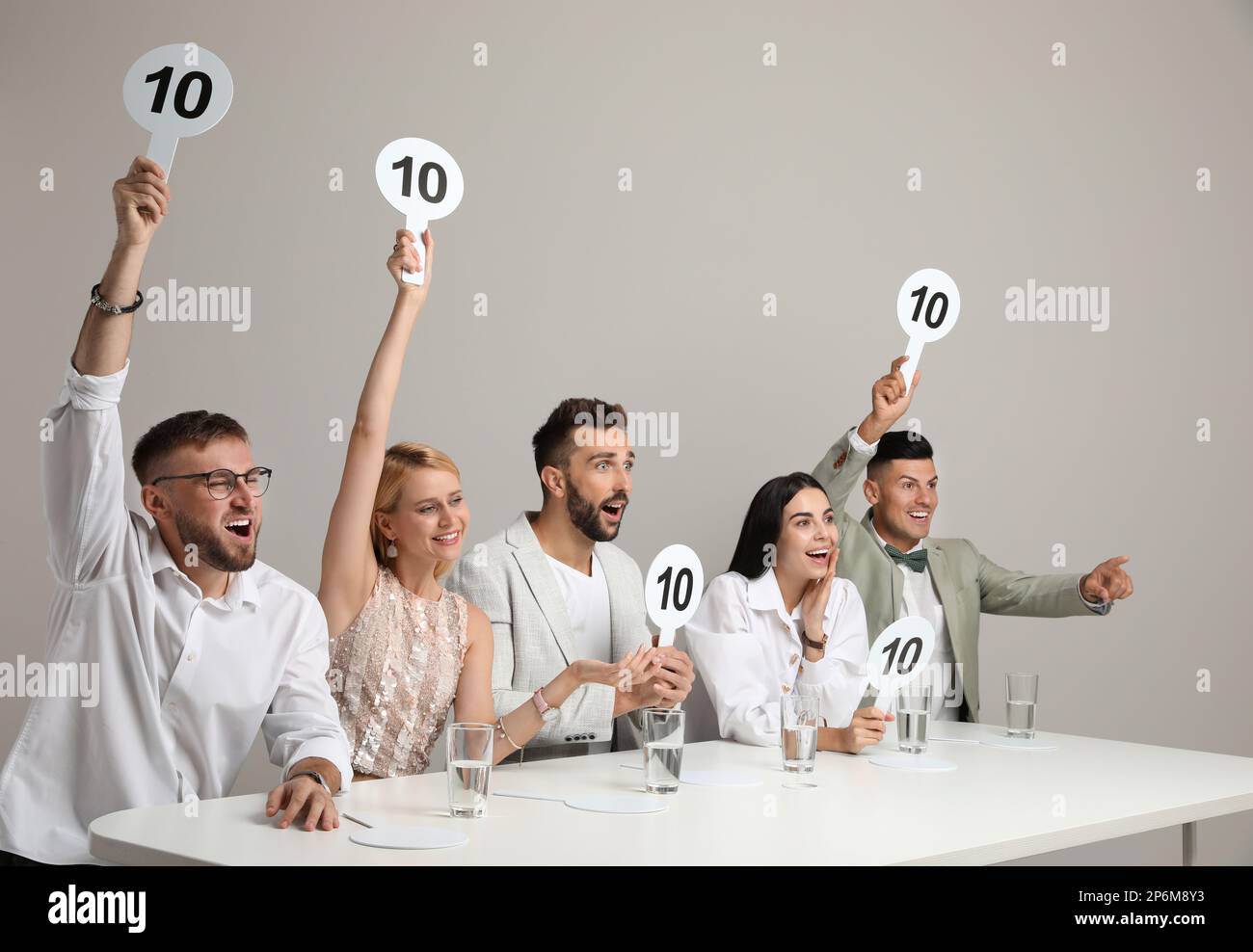 Panel of judges holding signs with highest score at table on beige ...