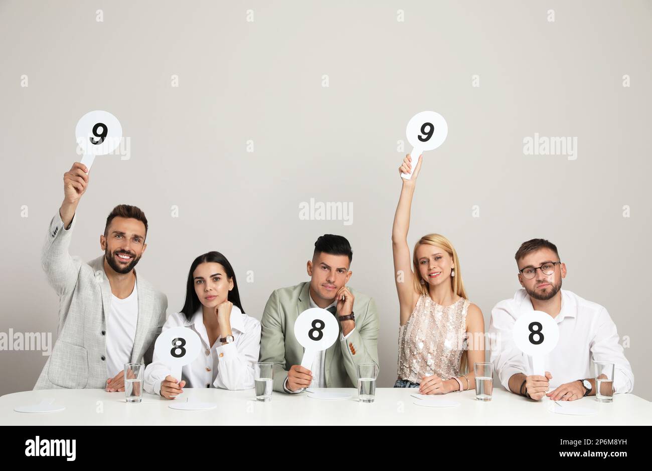 Panel of judges holding different score signs at table on beige ...