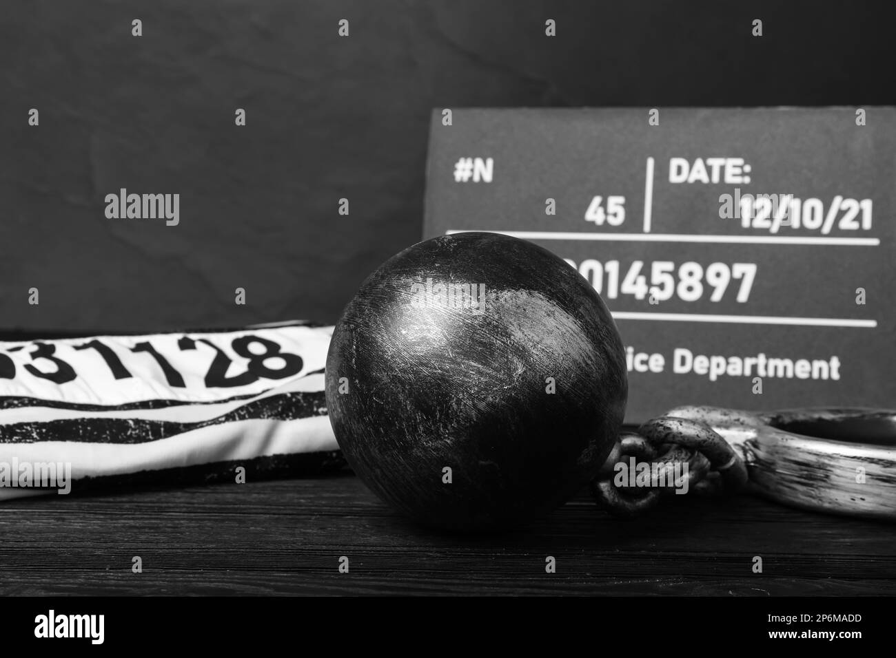 Metal ball with chain, prison uniform and mugshot letter board on black ...