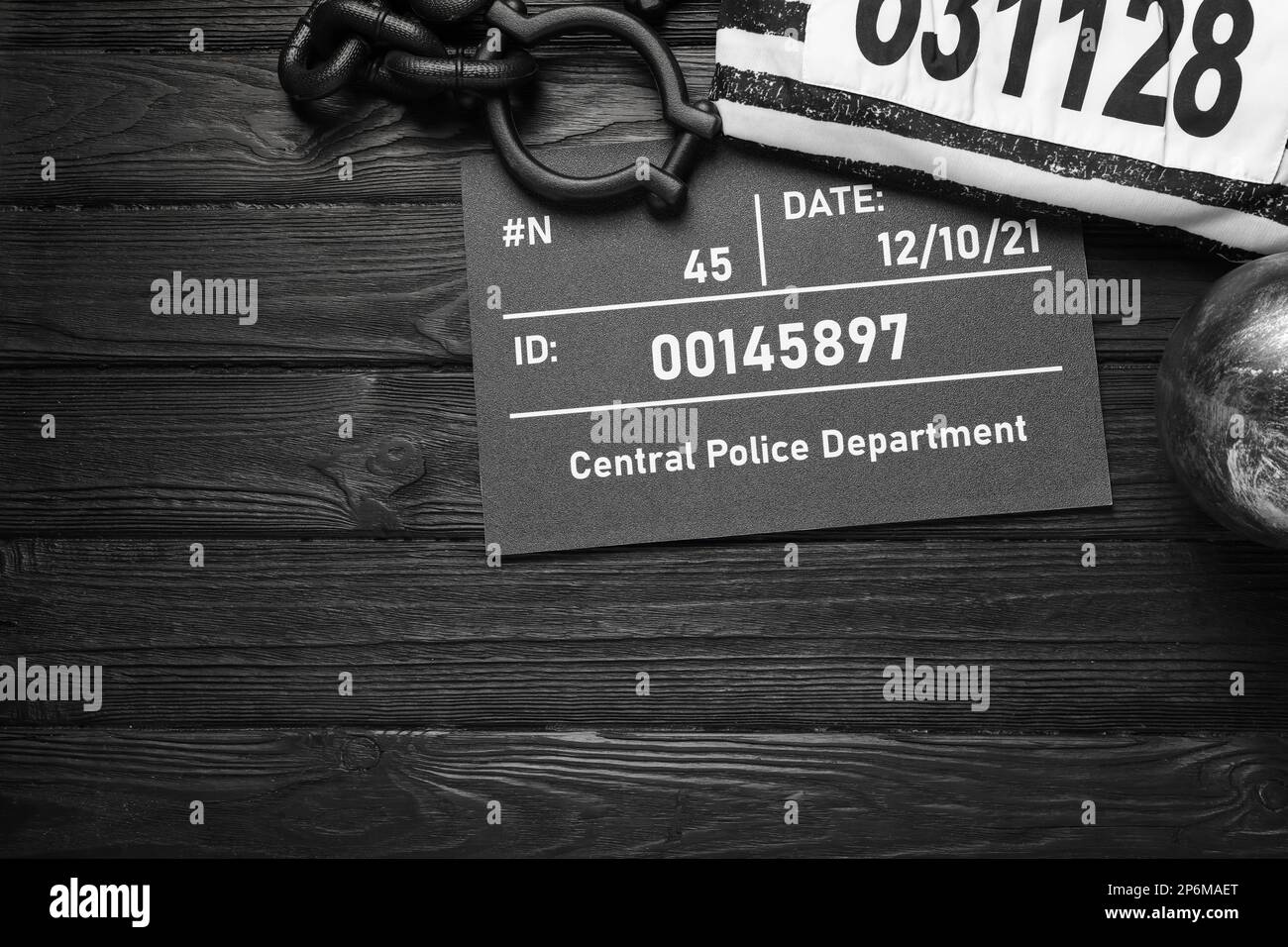 Metal ball with chain, prison uniform and mugshot letter board on black ...