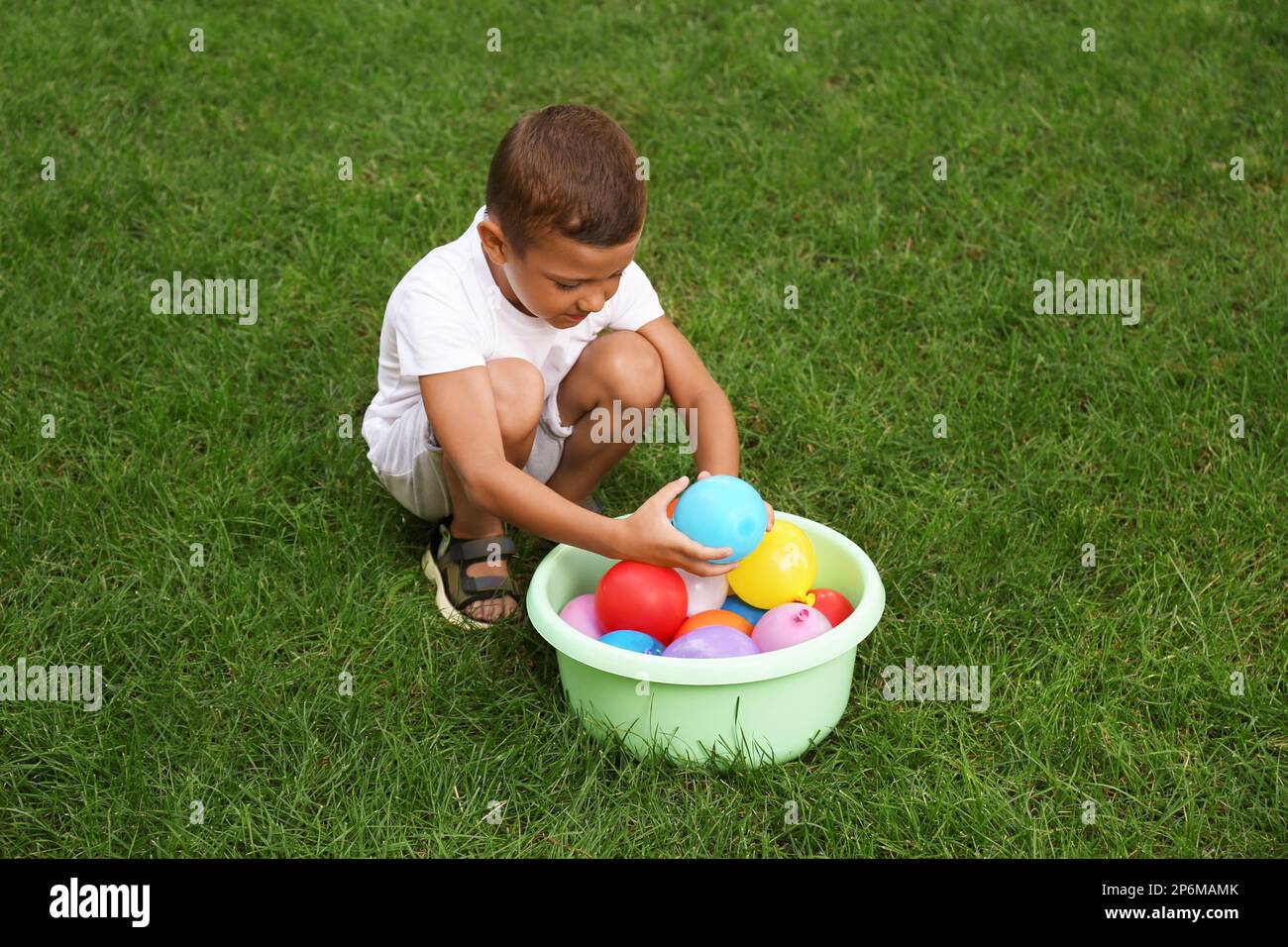 Little boy with basin of water bombs on green grass Stock Photo - Alamy