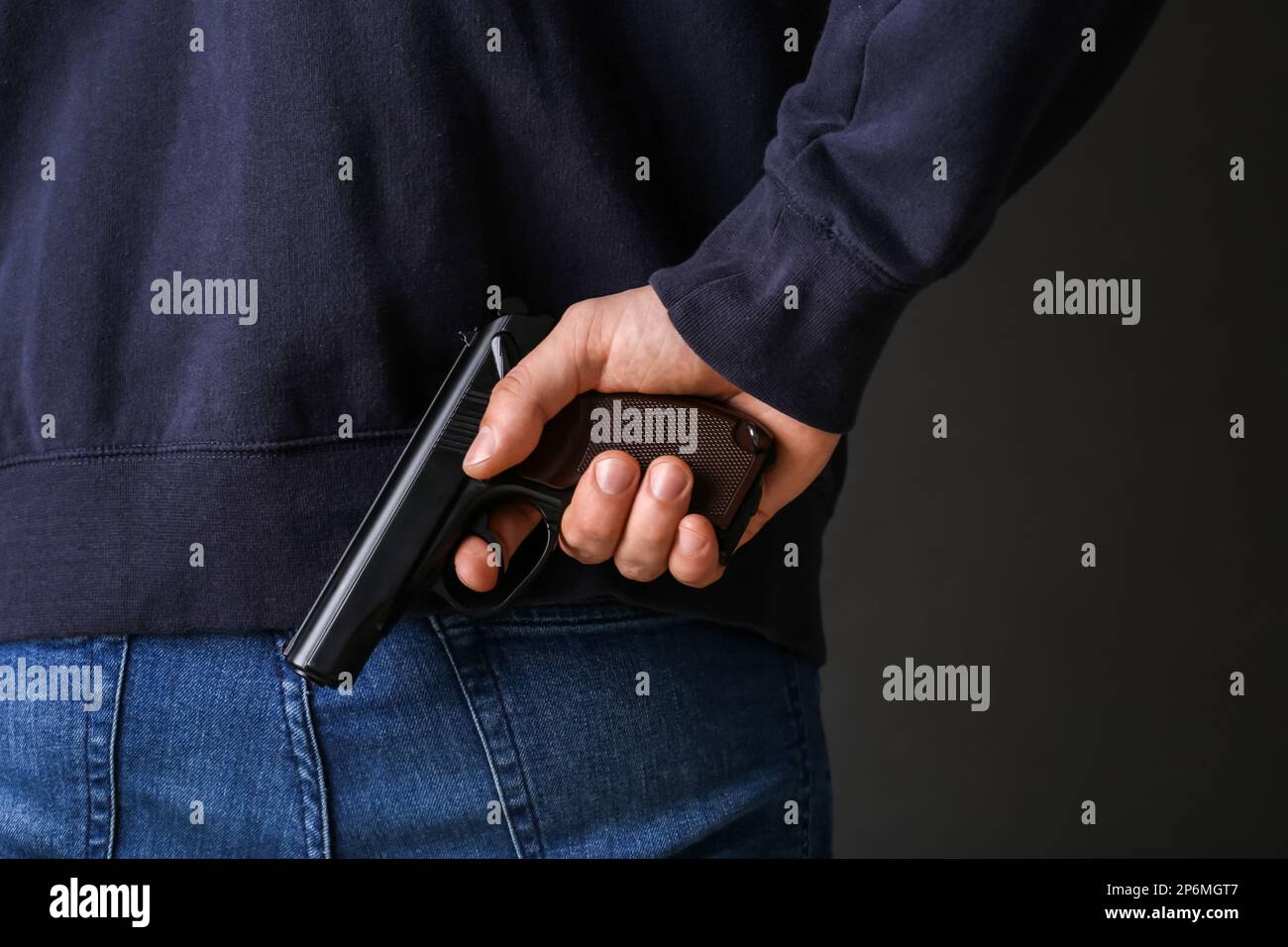 Man hiding gun behind his back on dark background, closeup Stock Photo ...
