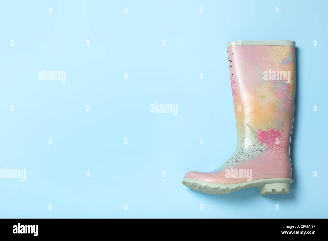 Colorful rubber boot on light blue background, top view. Space for text ...