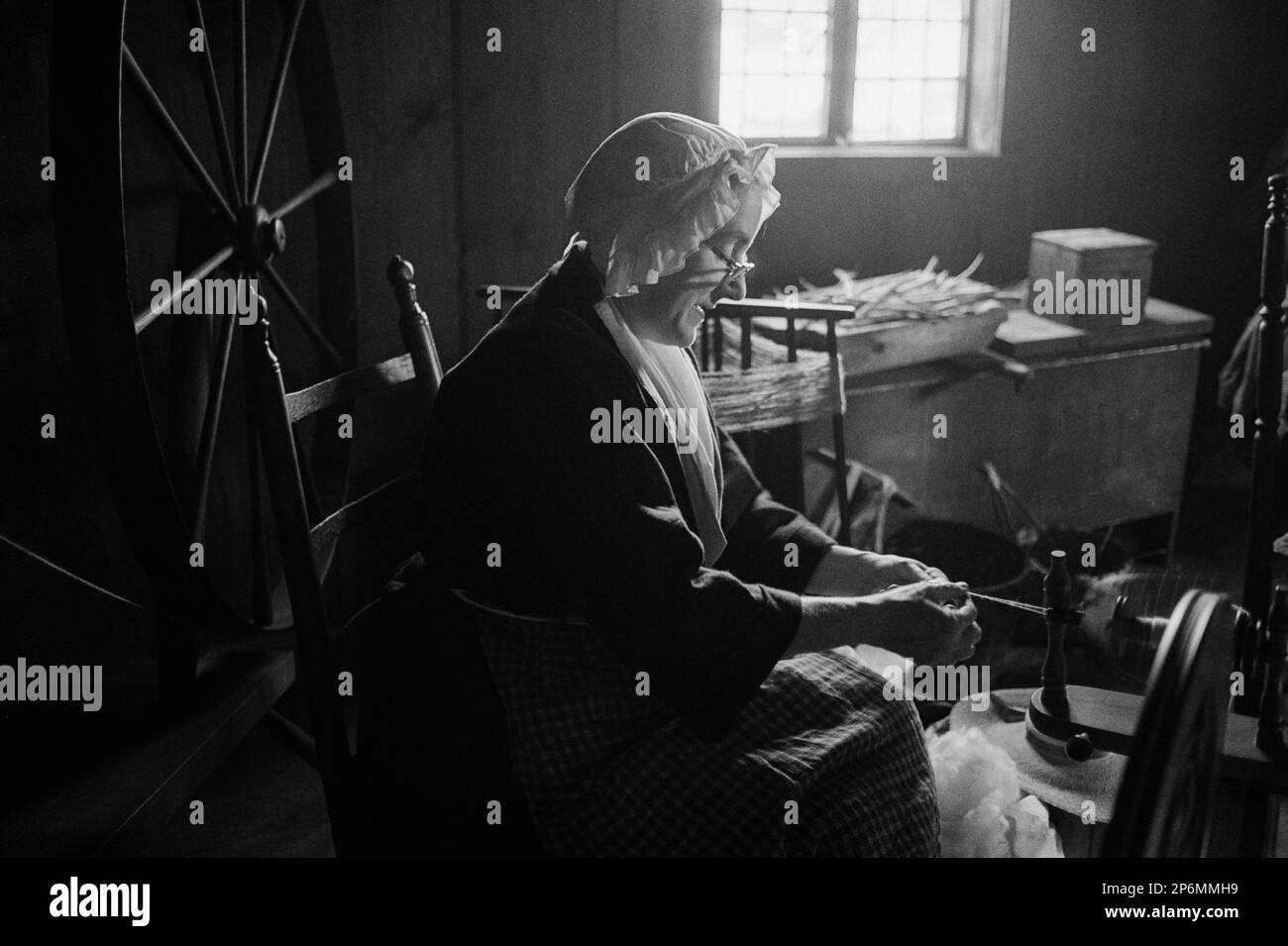 An actress in colonial costume works at a spinning wheel with wool in ...