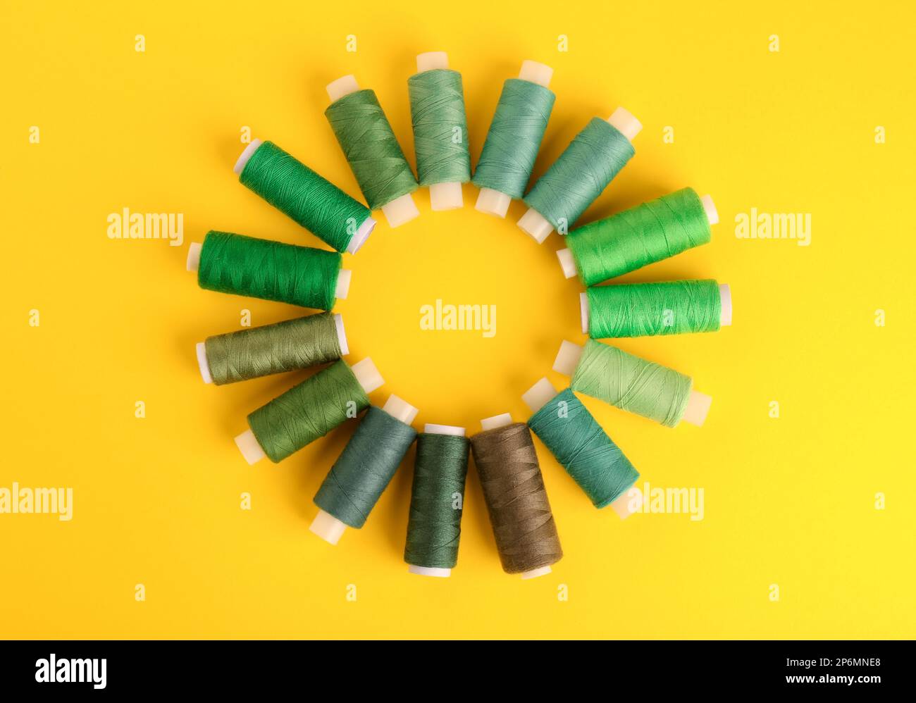 Different shades of green sewing threads on yellow background, flat lay ...