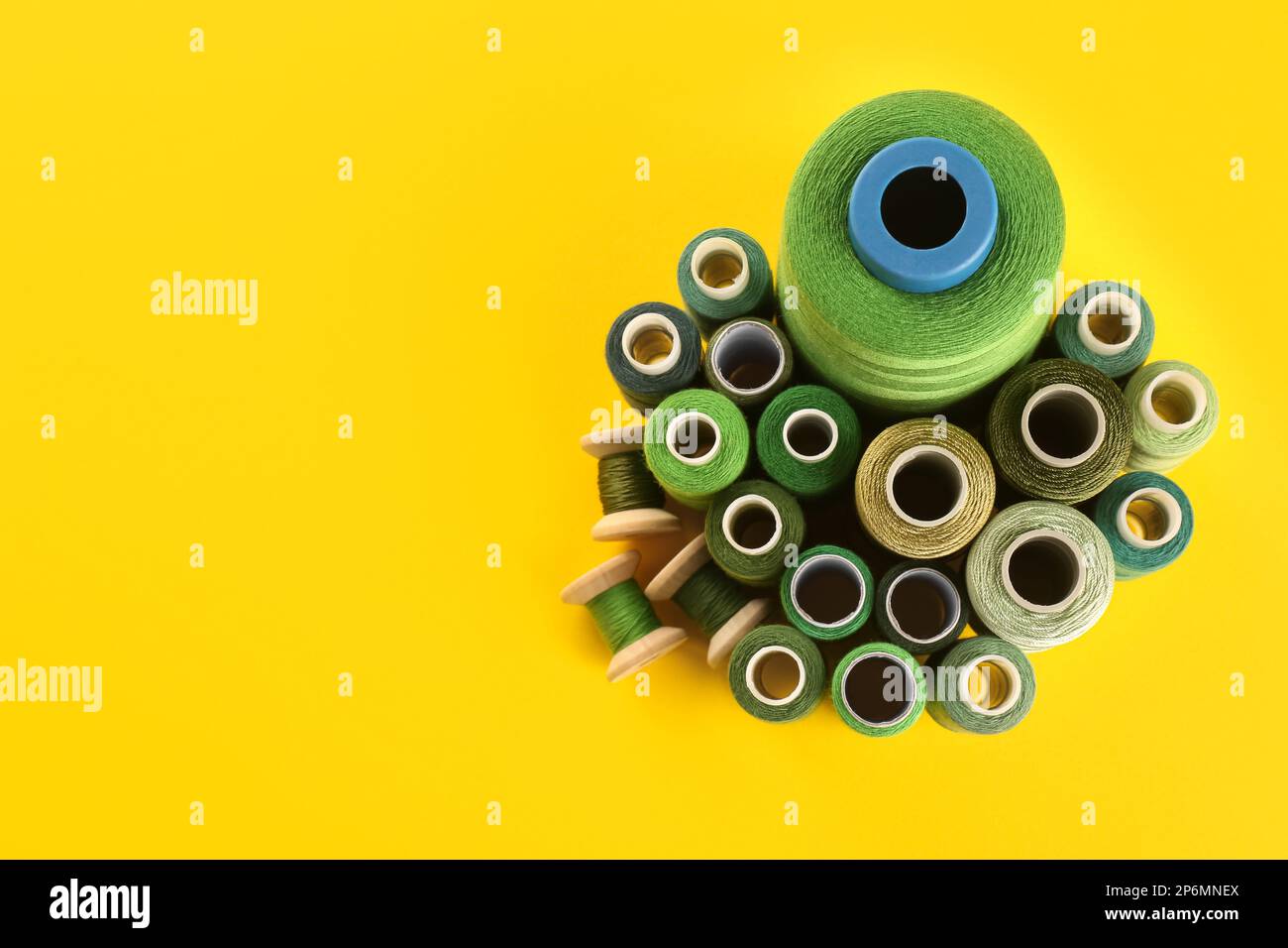 Different shades of green sewing threads on yellow background, flat lay ...