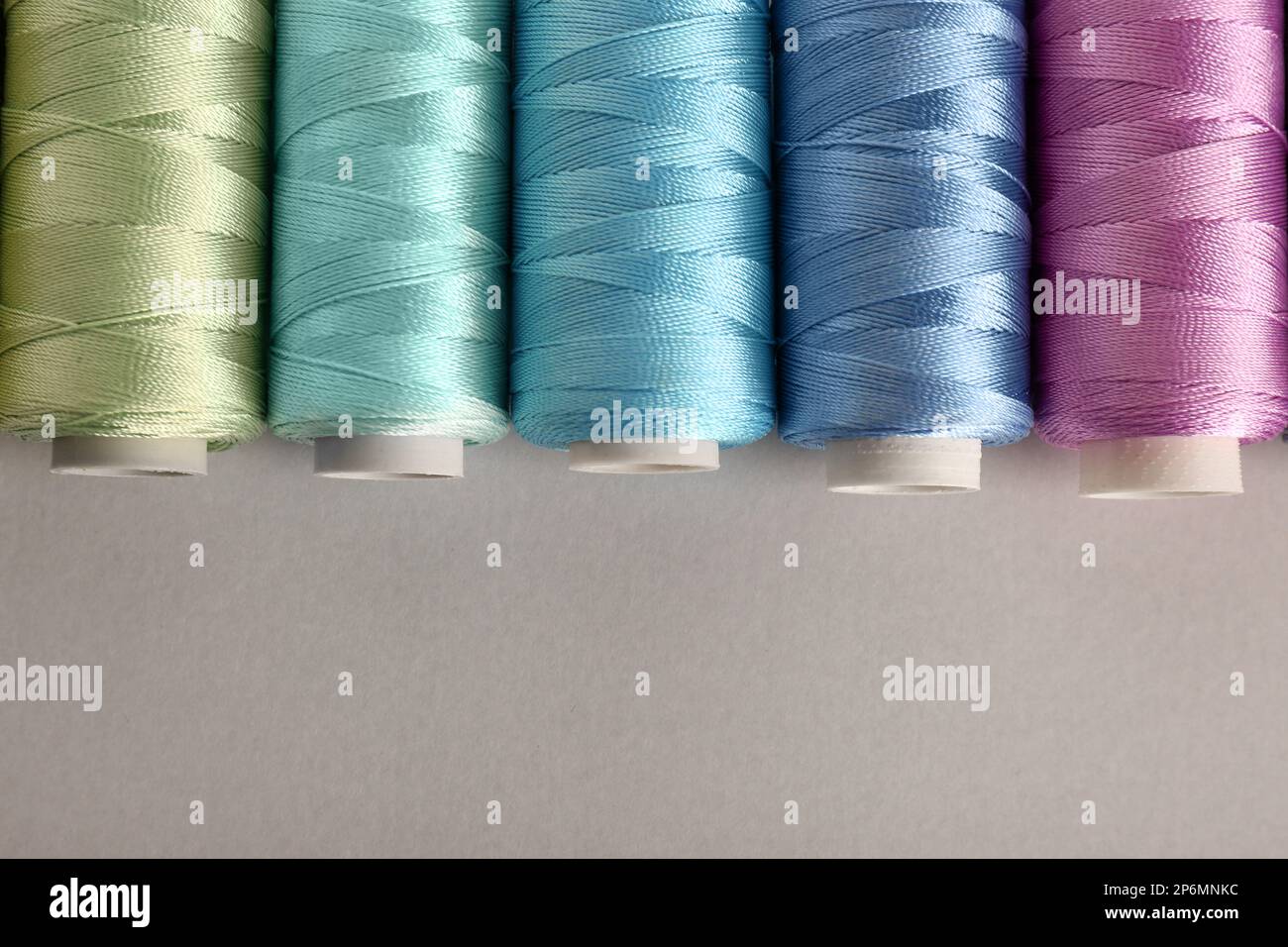 Different colorful sewing threads on light grey background, flat lay ...