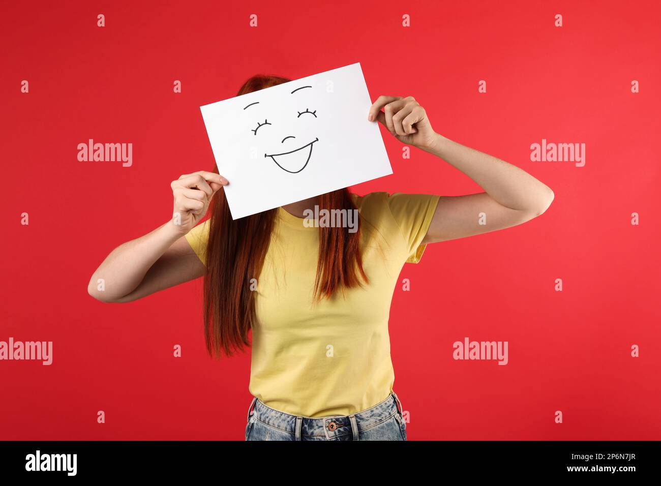 Woman hiding behind sheet of paper with happy face on red background ...
