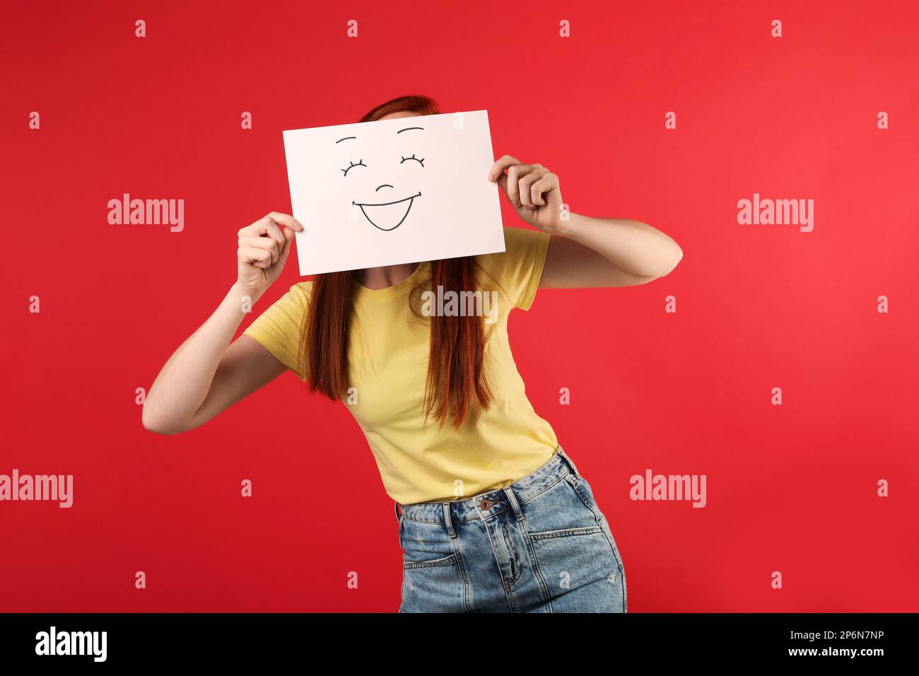 Woman hiding behind sheet of paper with happy face on red background ...