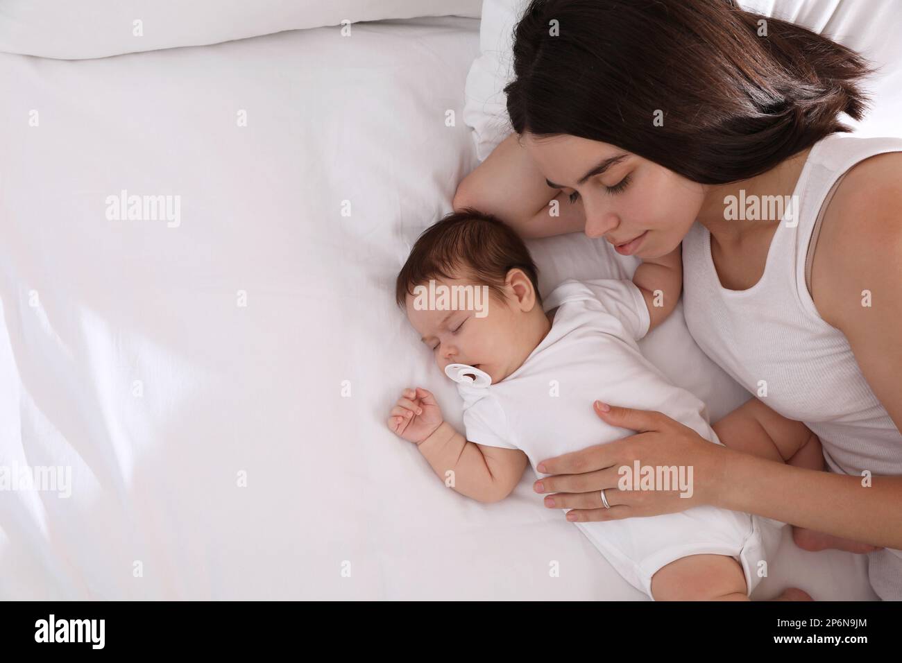 Young mother resting near her sleeping baby on bed, top view. Space for ...