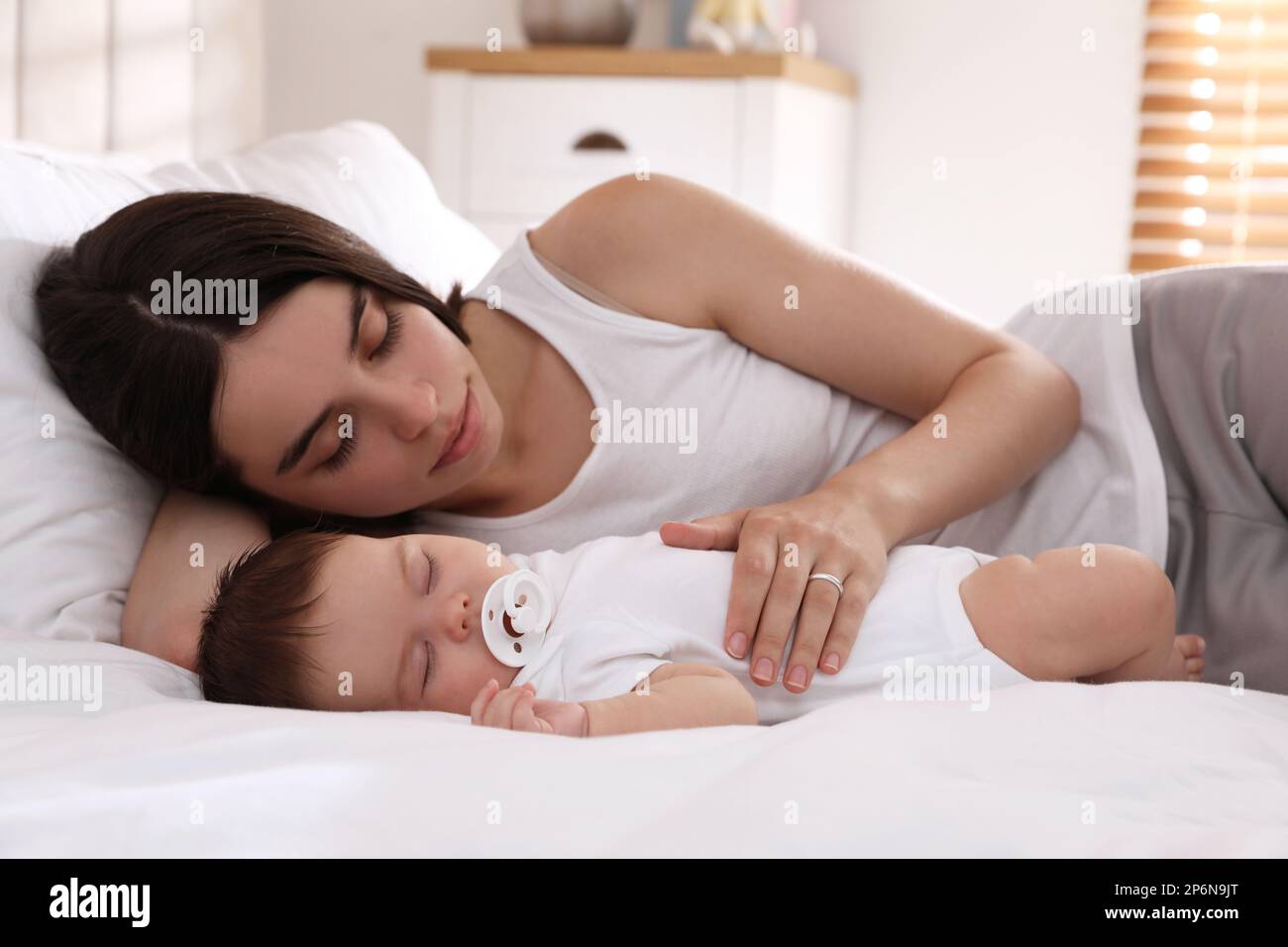 Young mother resting near her sleeping baby on bed at home Stock Photo ...